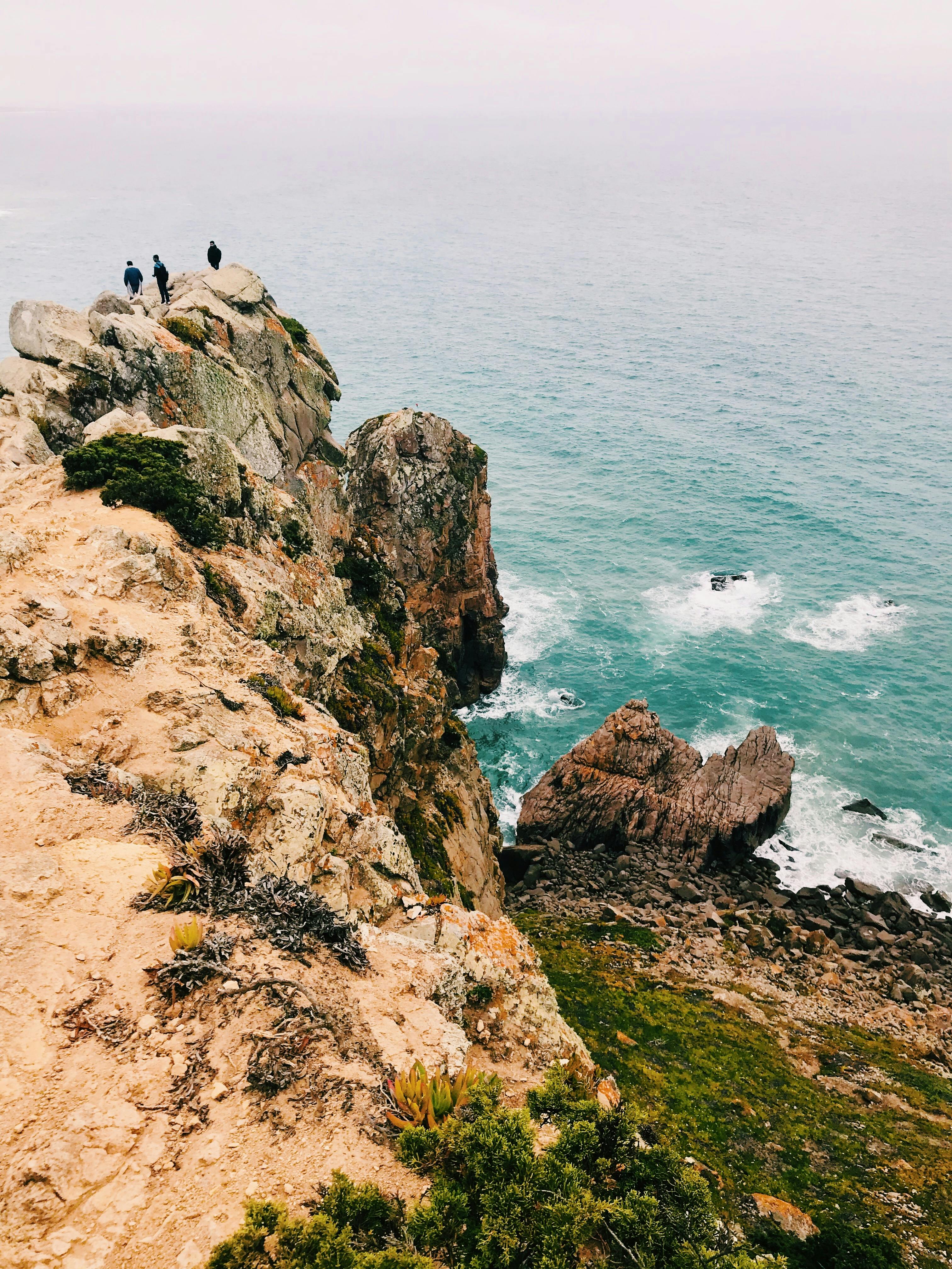 Three Men Standing on Top of Cliff in Beach · Free Stock Photo