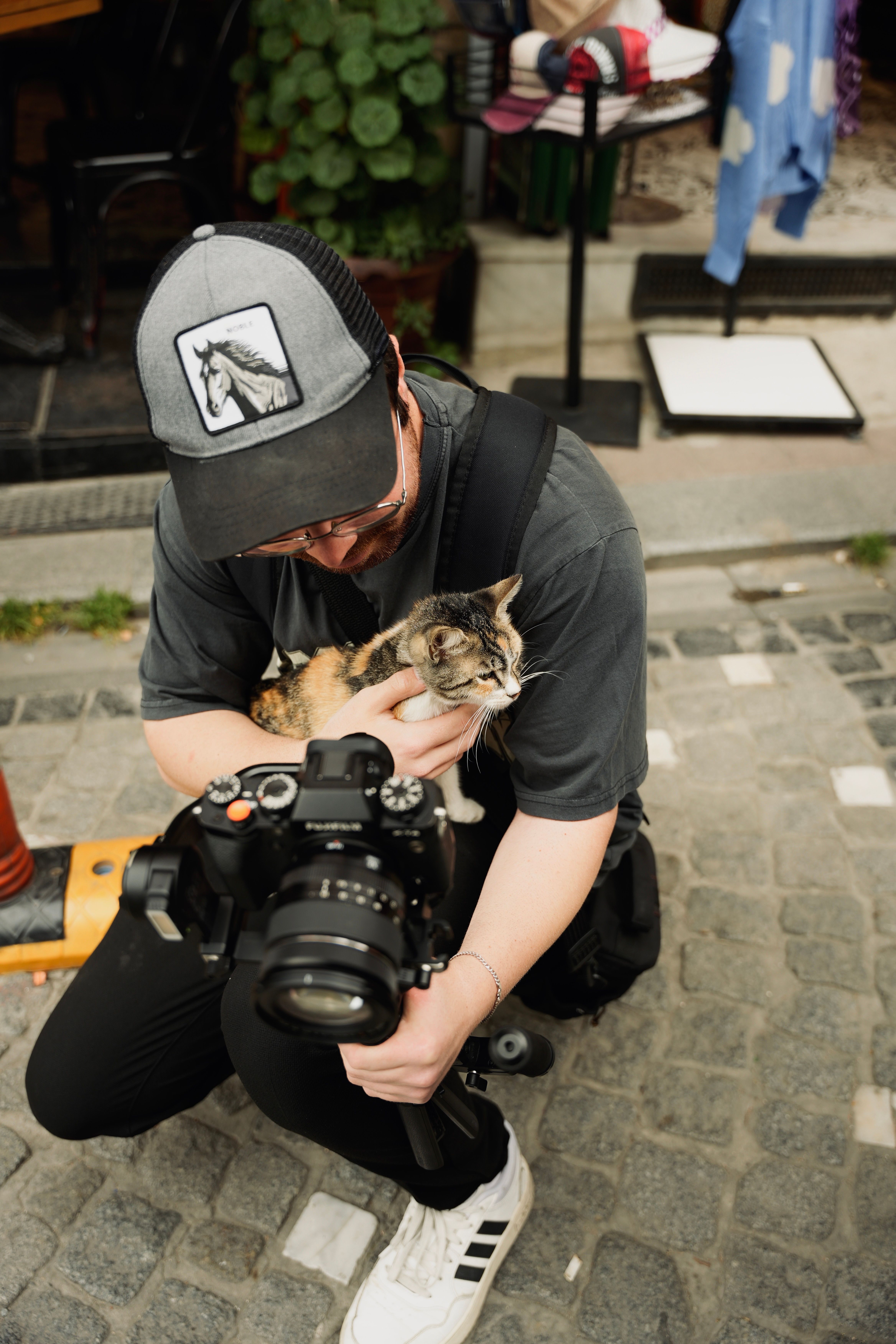 Man in Cap and with Camera Squatting and Holding Kitten · Free Stock Photo