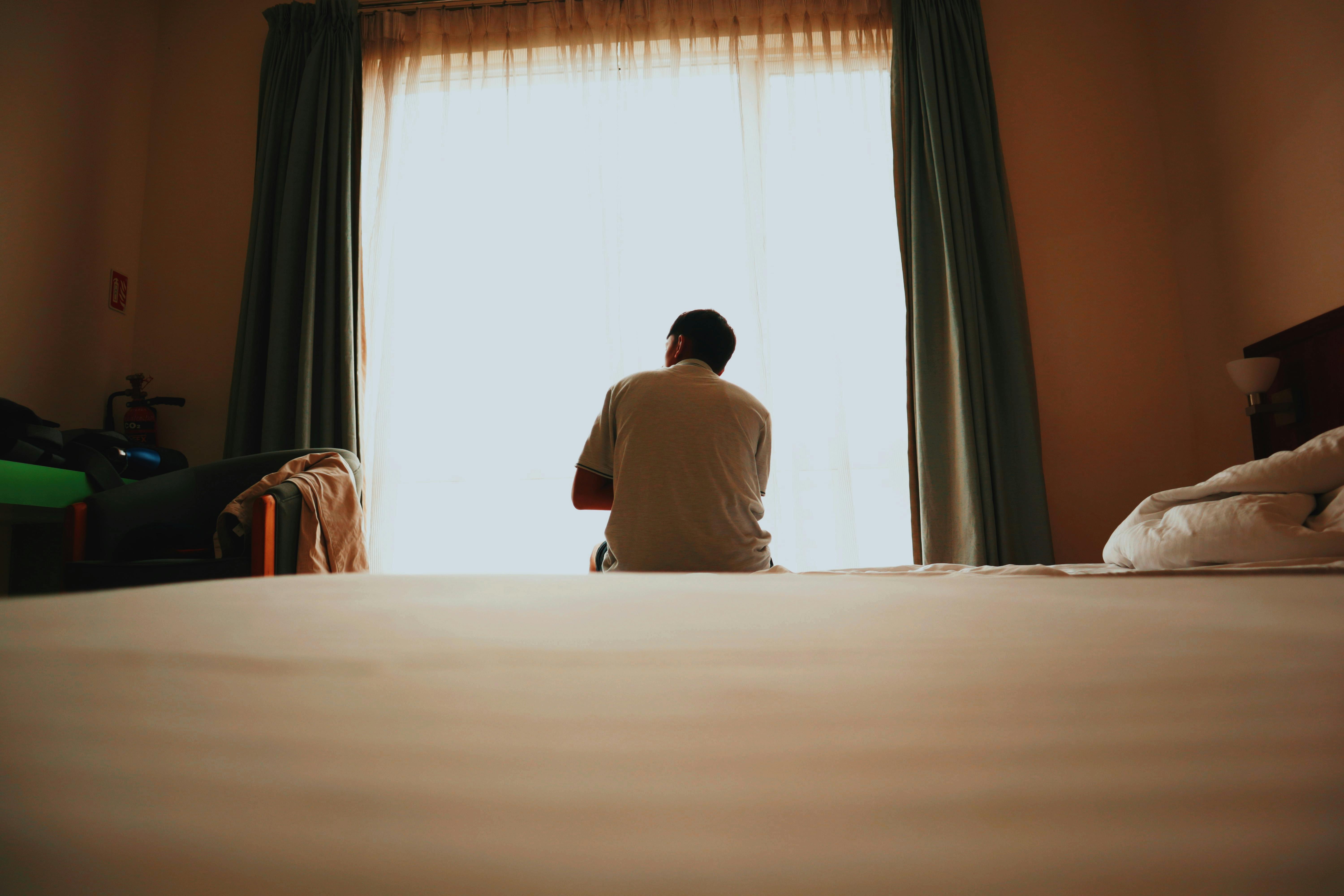 Man Sitting against Window with Curtains · Free Stock Photo