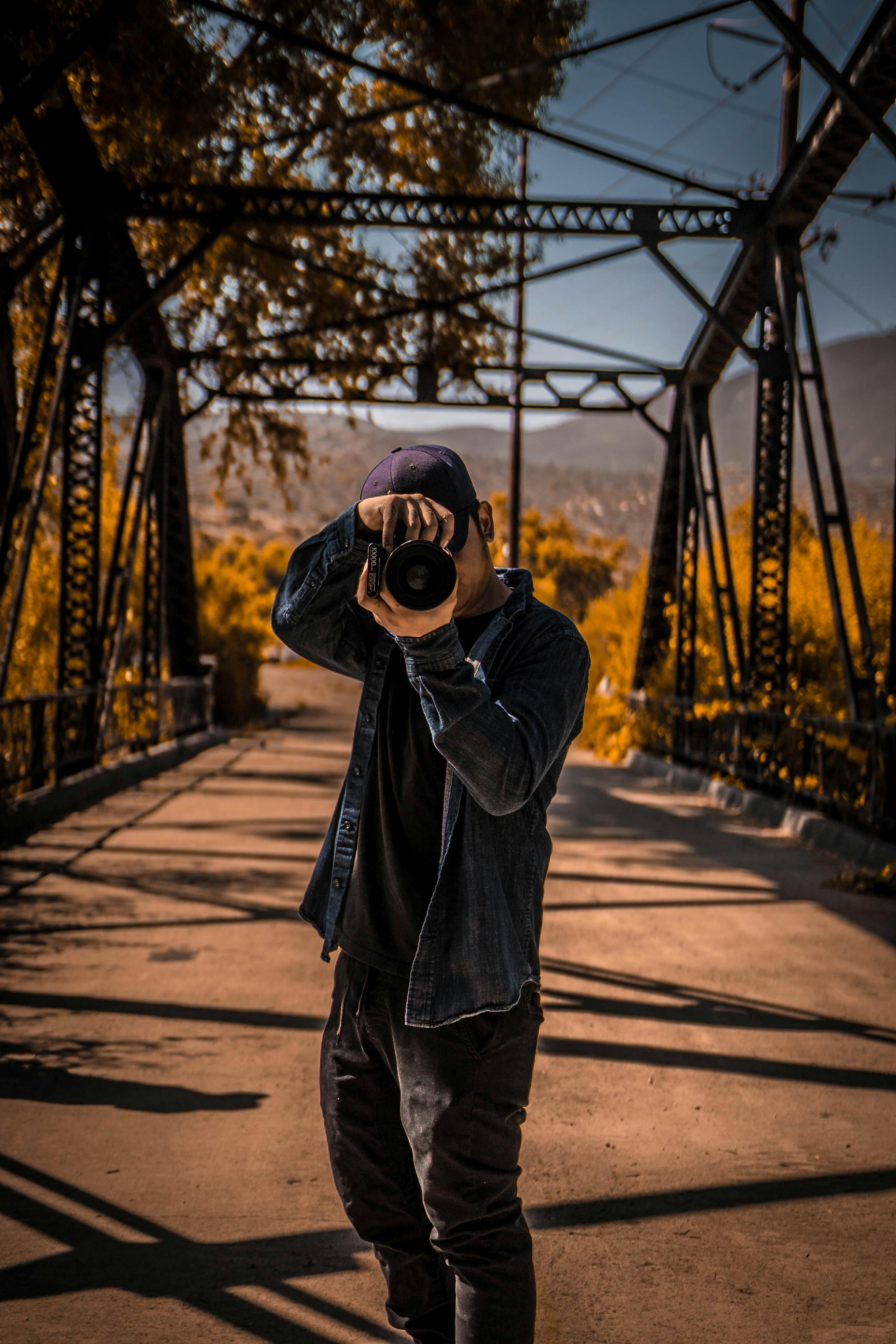 Man Standing On Bridge Holding Camera · Free Stock Photo