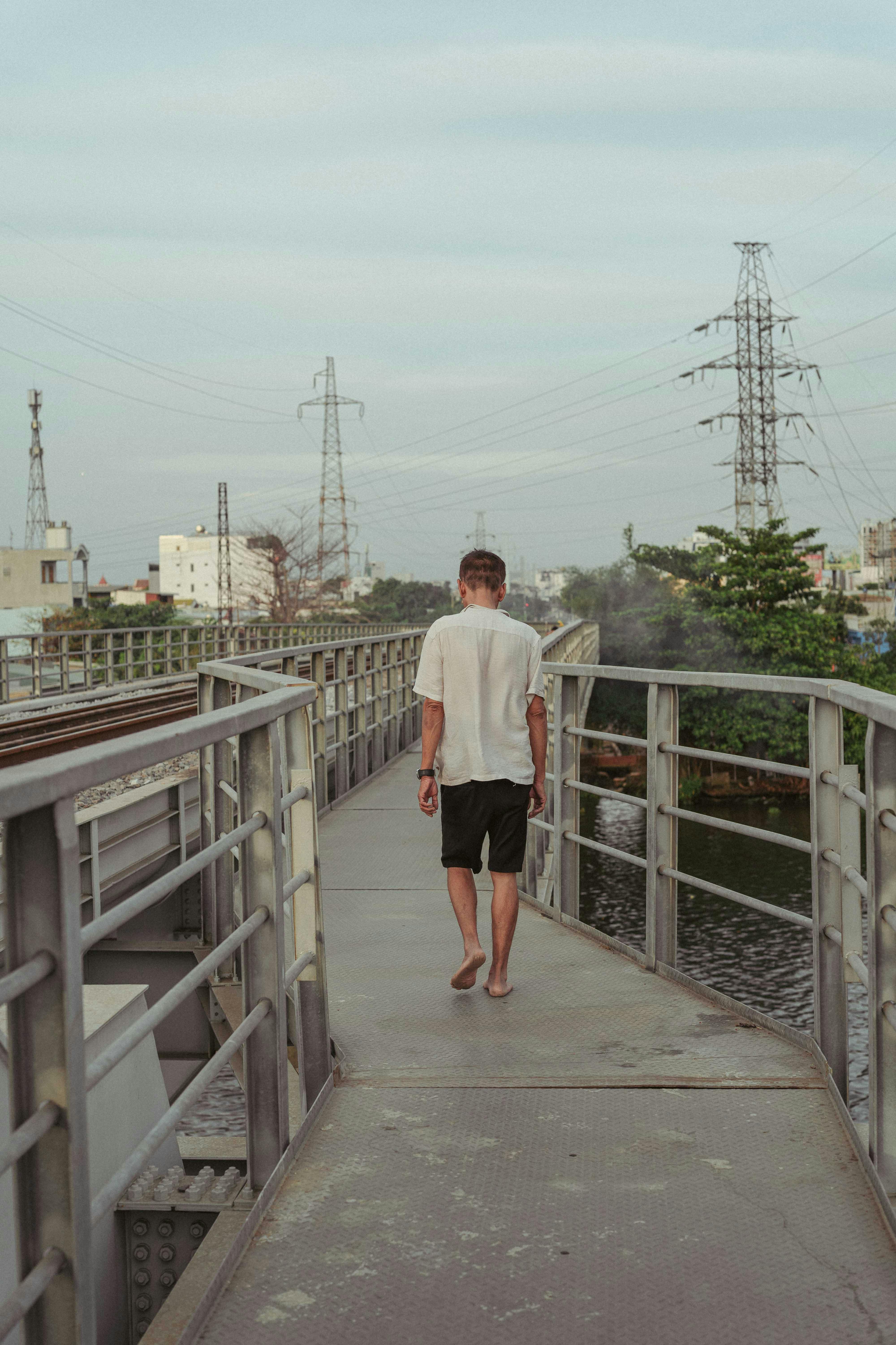 Back View of Man Walking on Steel Bridge Barefoot · Free Stock Photo