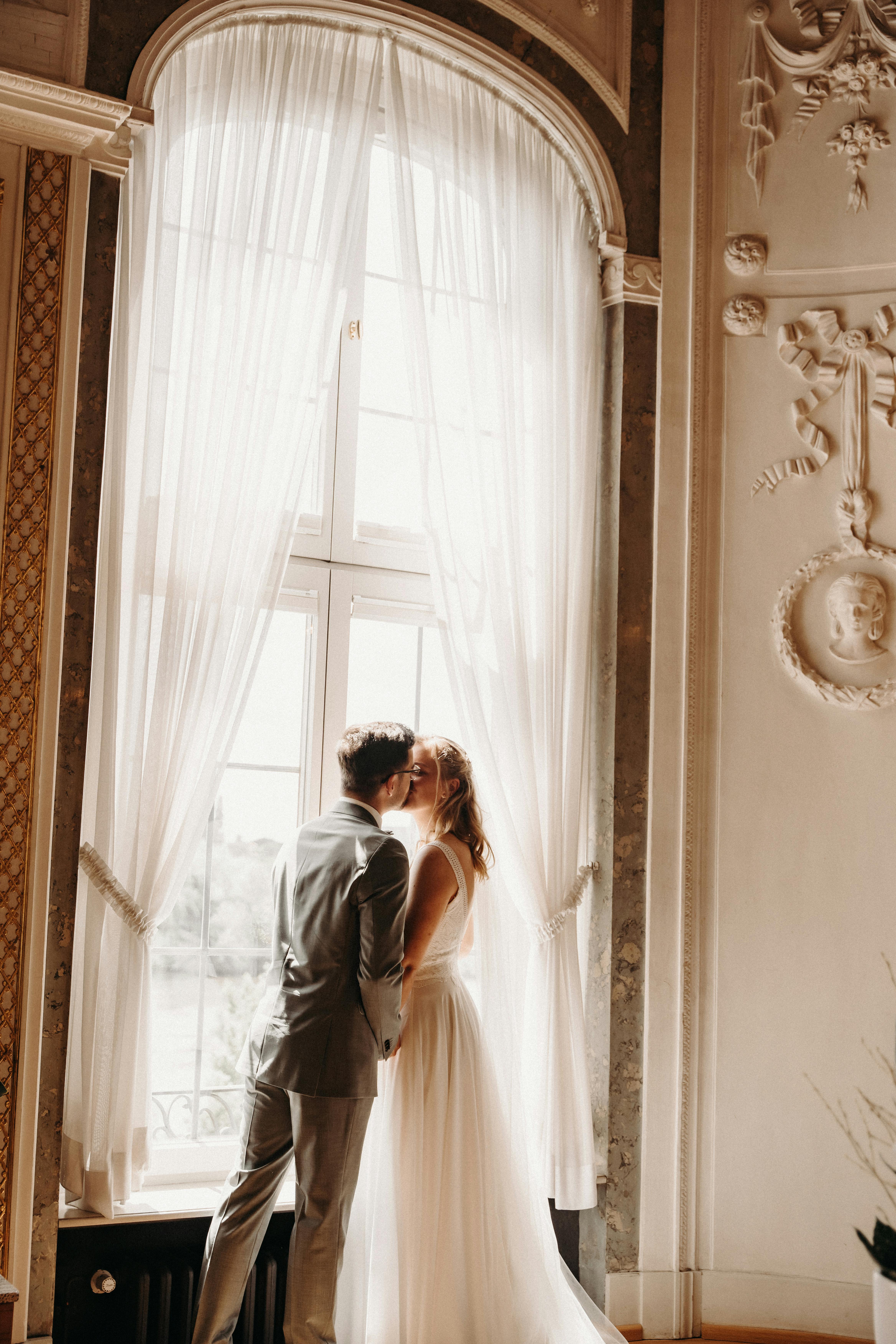 Newlywed Couple Kissing near Window · Free Stock Photo