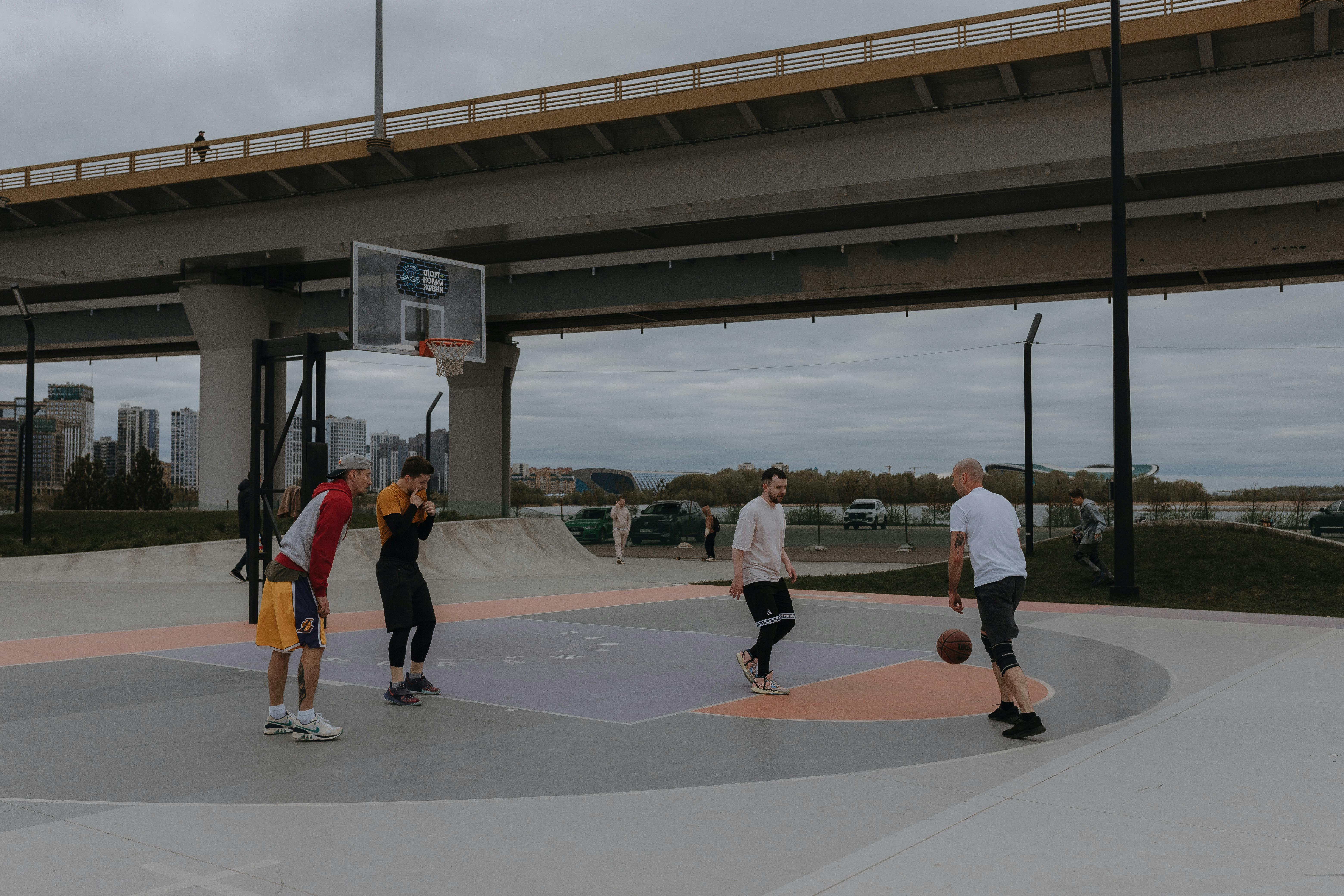 Men Playing Basketball in an Outdoor Court with a Bridge in the ...