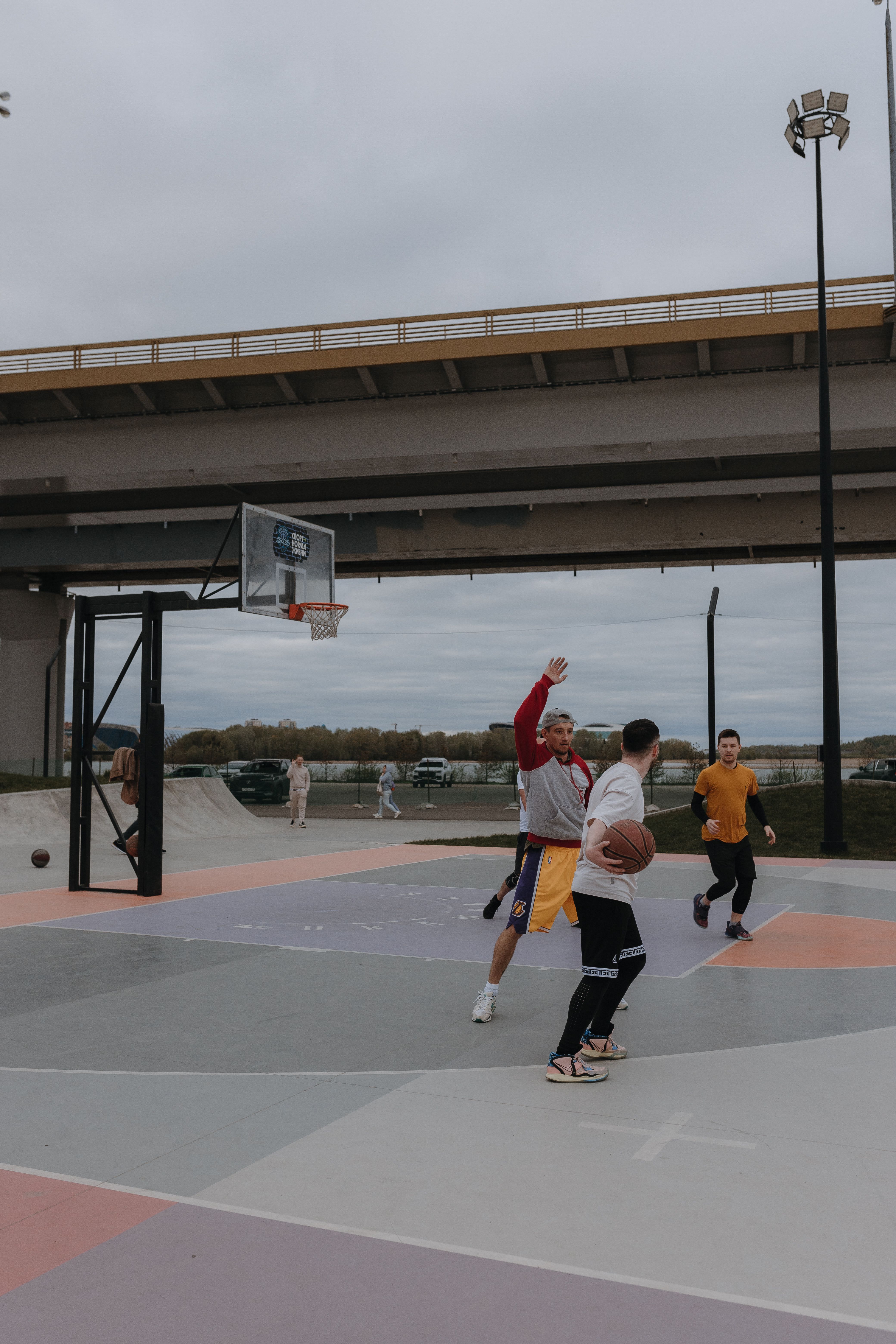 People playing basketball on a court under a bridge · Free Stock Photo