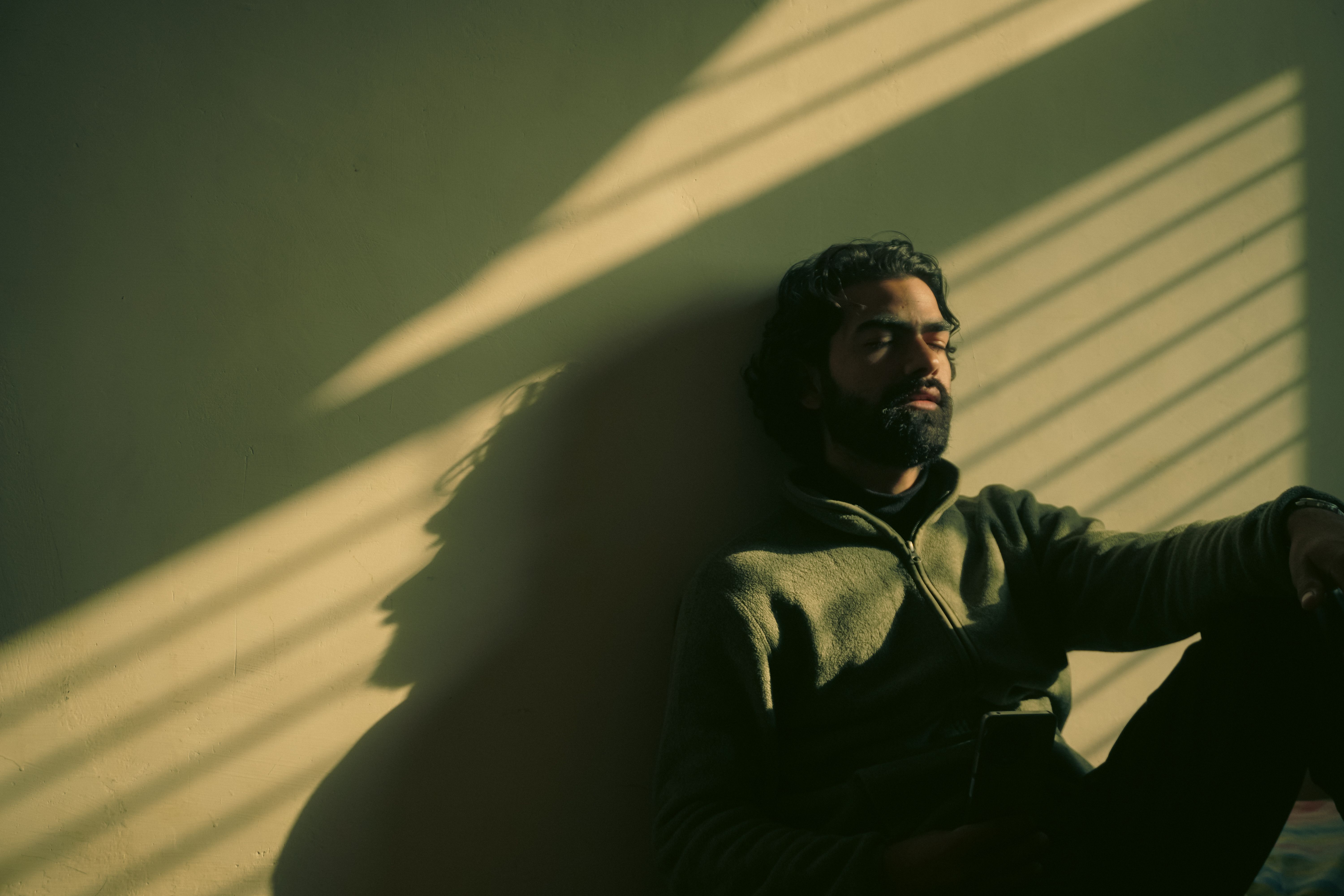 A Bearded Man Sitting by the Wall in Sunlight · Free Stock Photo