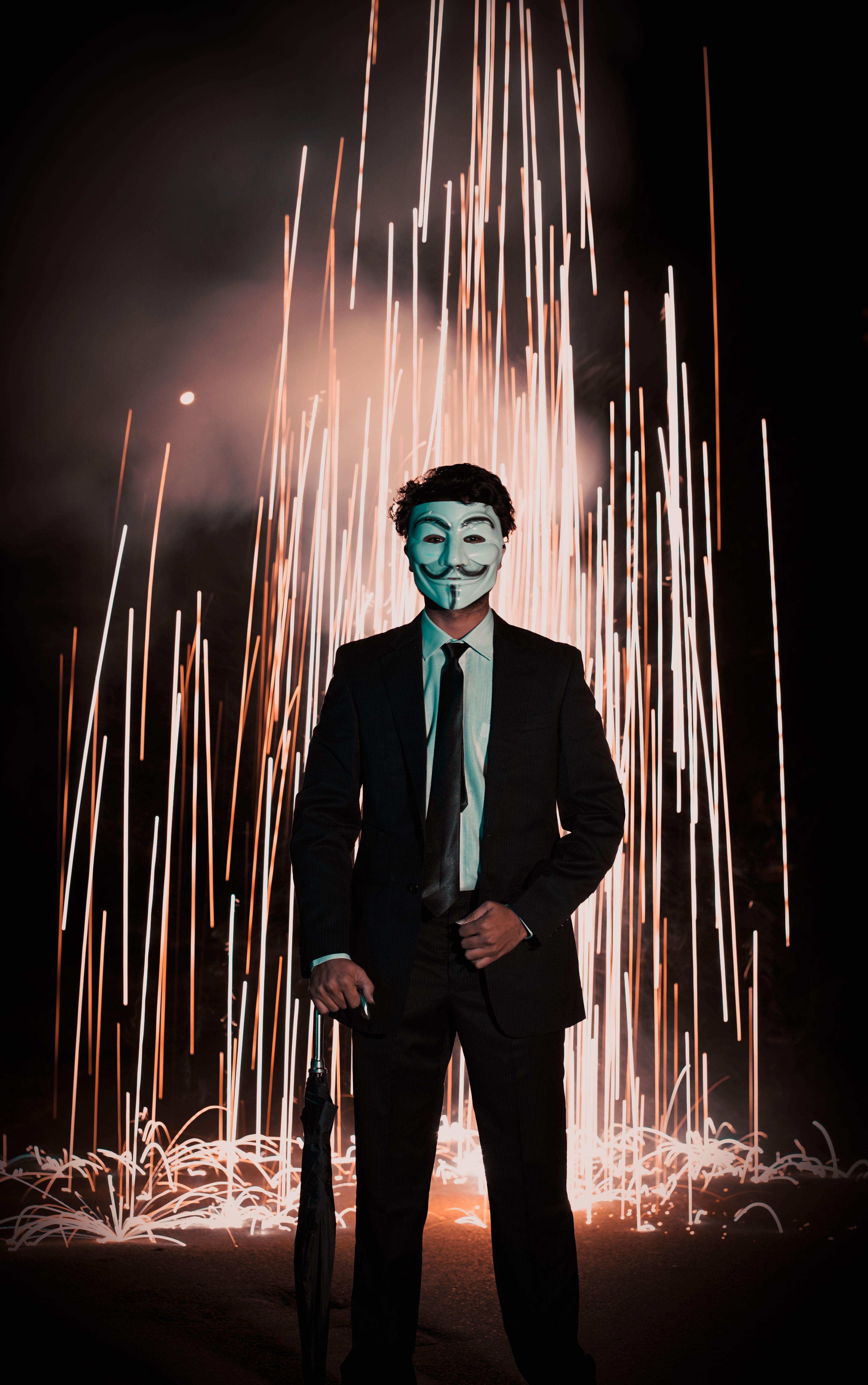 Man in a Black Suit and an Anonymous Mask Standing with an Umbrella in ...