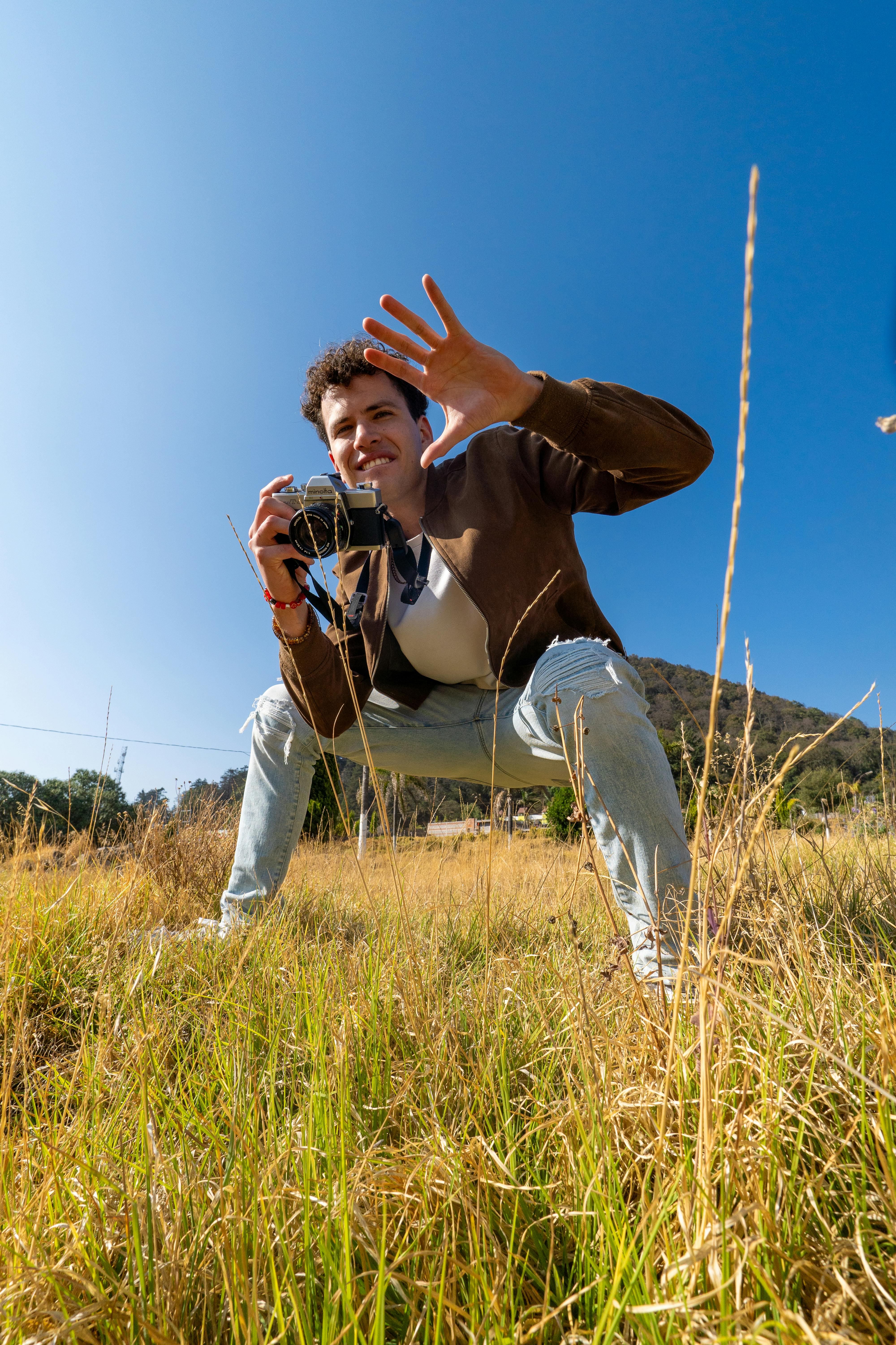 Photographer Crouching with a Camera in his Hand and Waving · Free ...