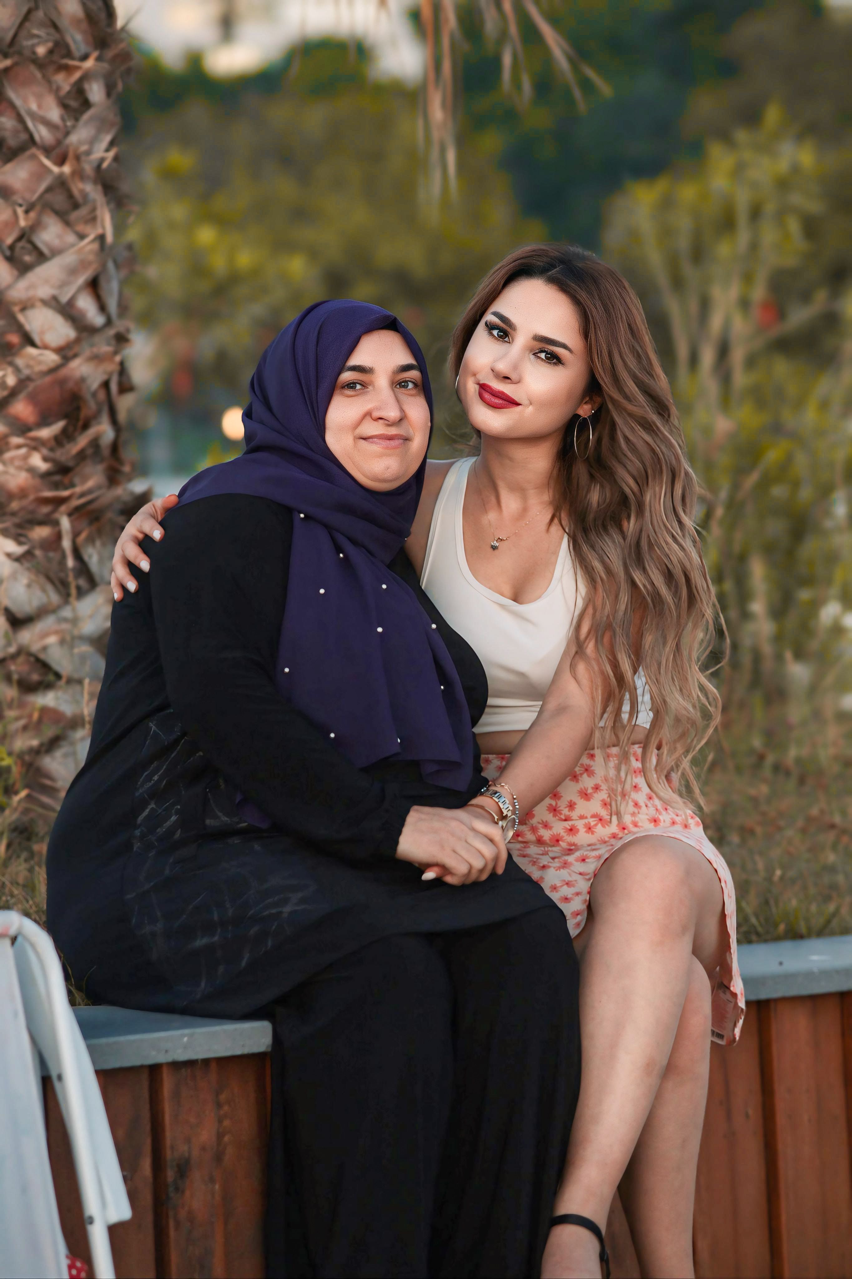 Women in Hijab and in Tank Top Sitting Together on Wall · Free Stock Photo