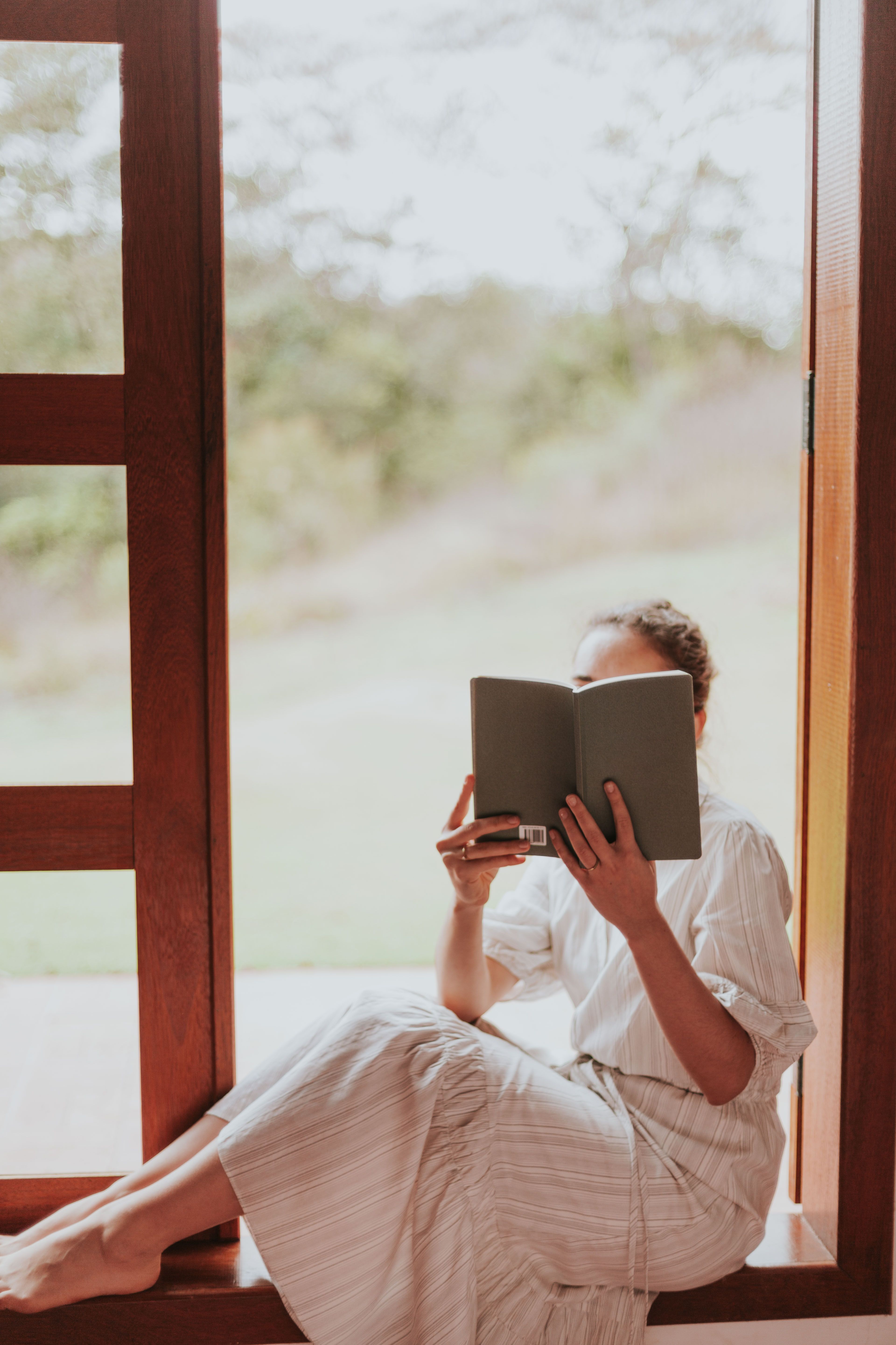 Woman in White Dress Sitting and Reading Book in Window · Free Stock Photo