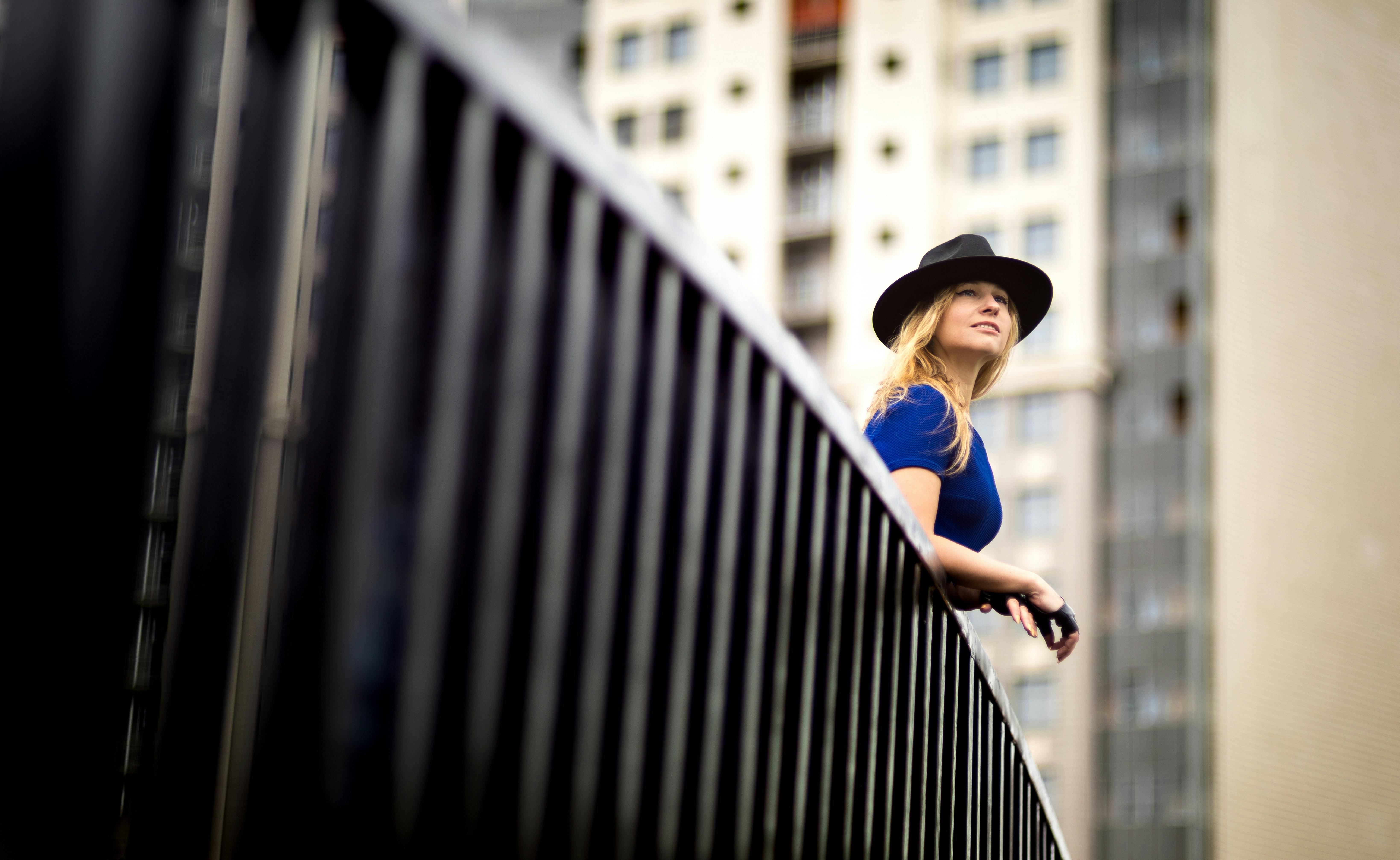 Woman wearing blue top and a hat leaning on metal railing · Free Stock ...
