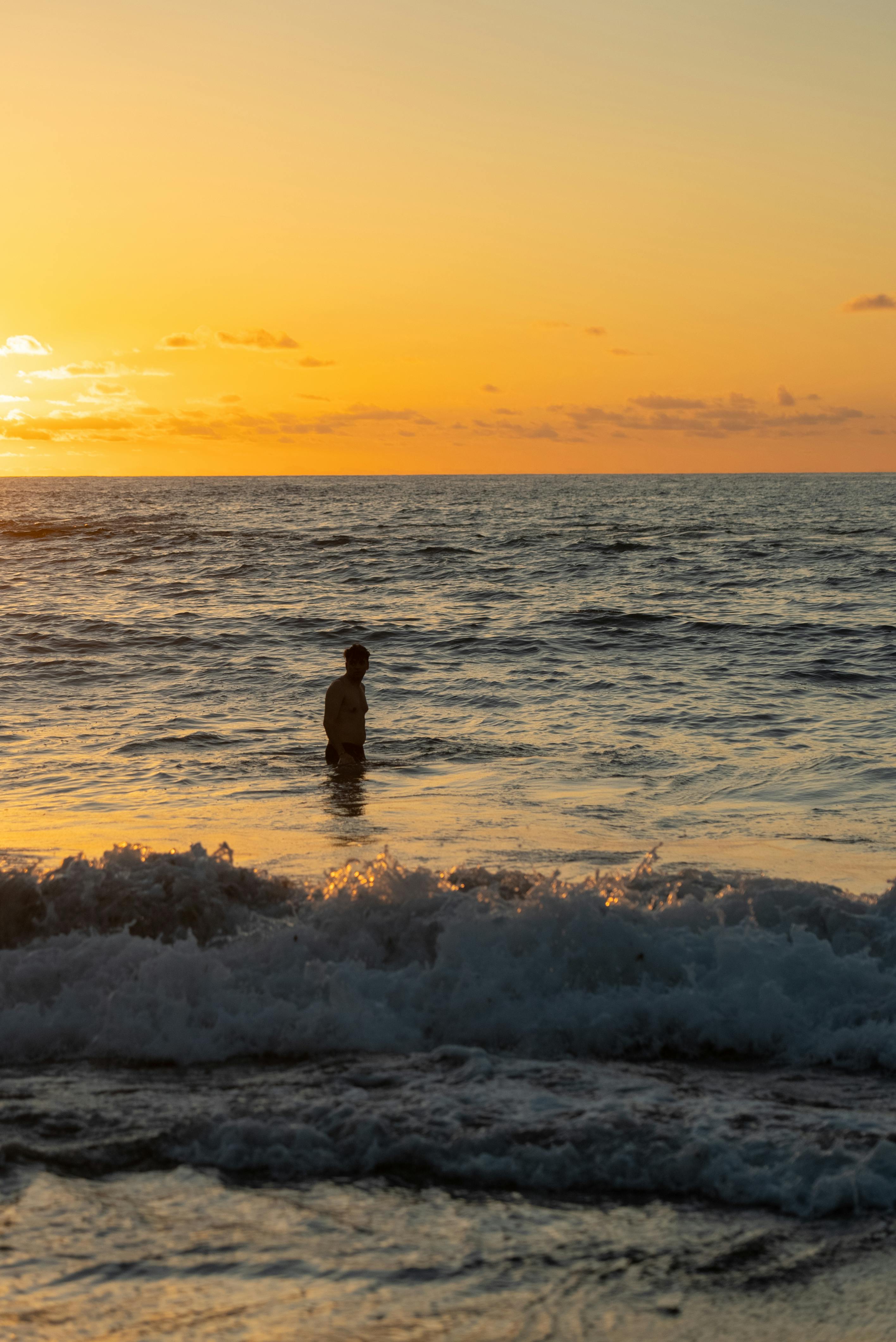 Man Standing Waist Deep in Coastal Water at Sunset · Free Stock Photo
