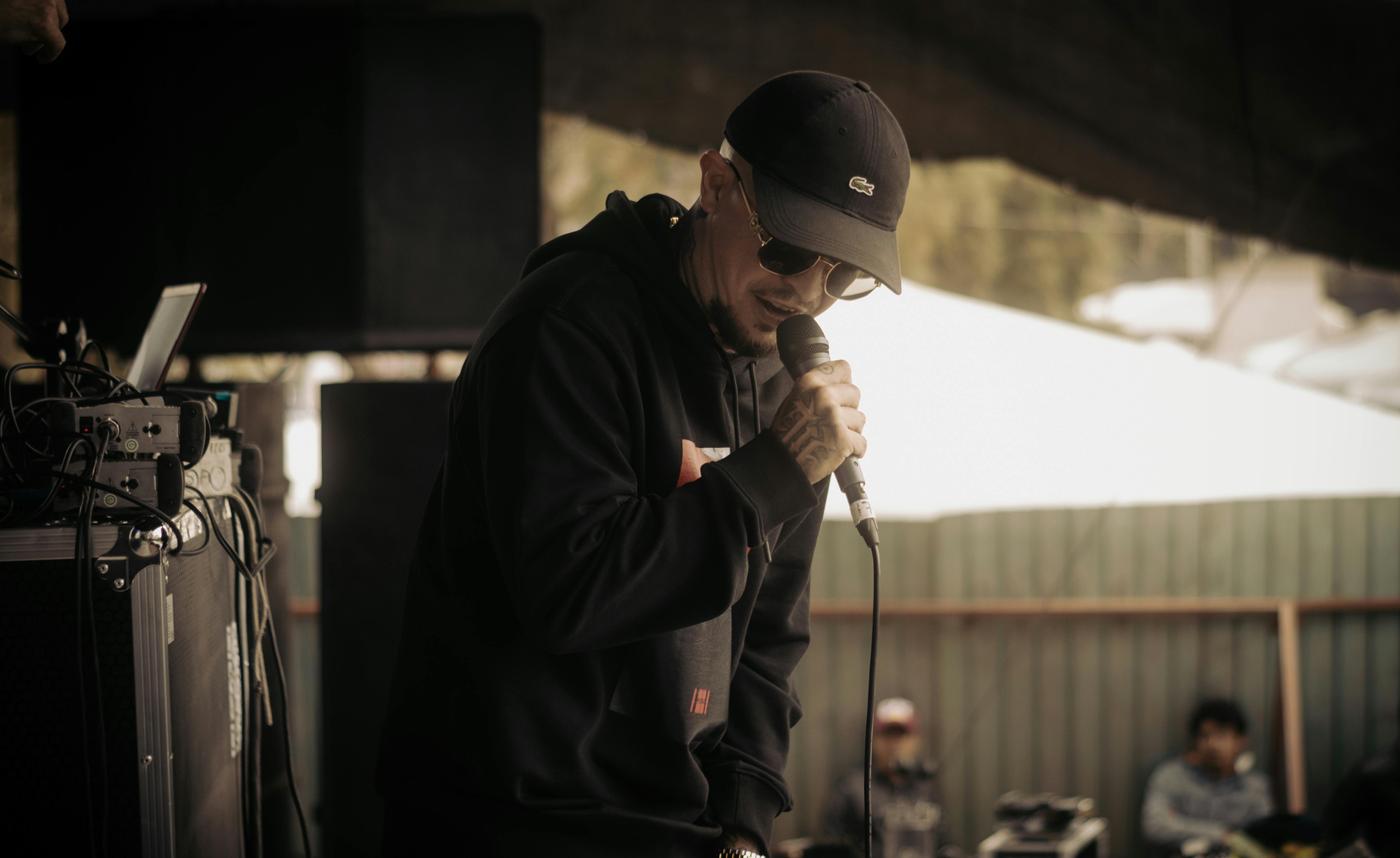 Man in Cap and Hoodie Singing with Microphone · Free Stock Photo