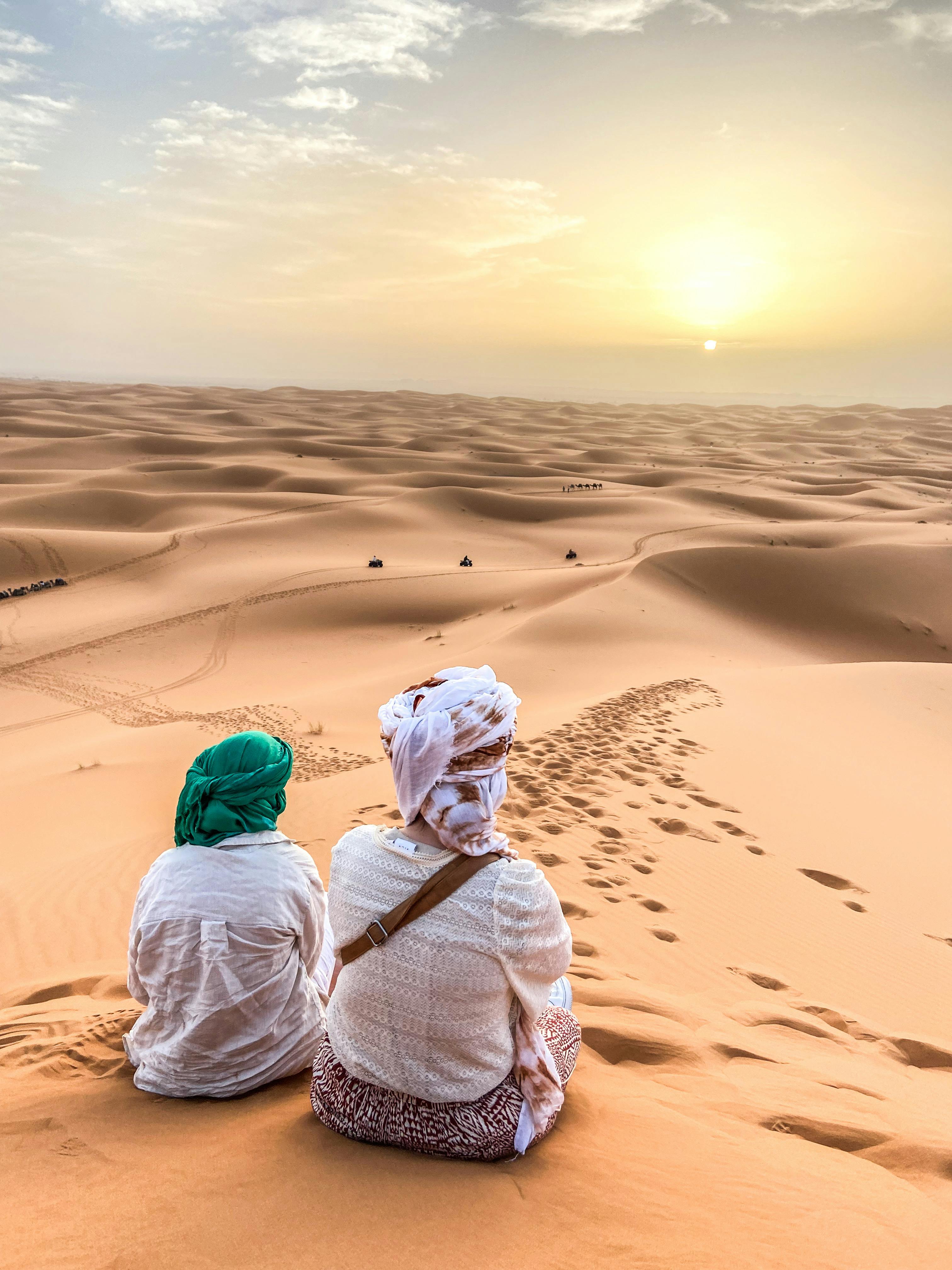Back View of Two People in Turbans Sitting in the Desert · Free Stock Photo