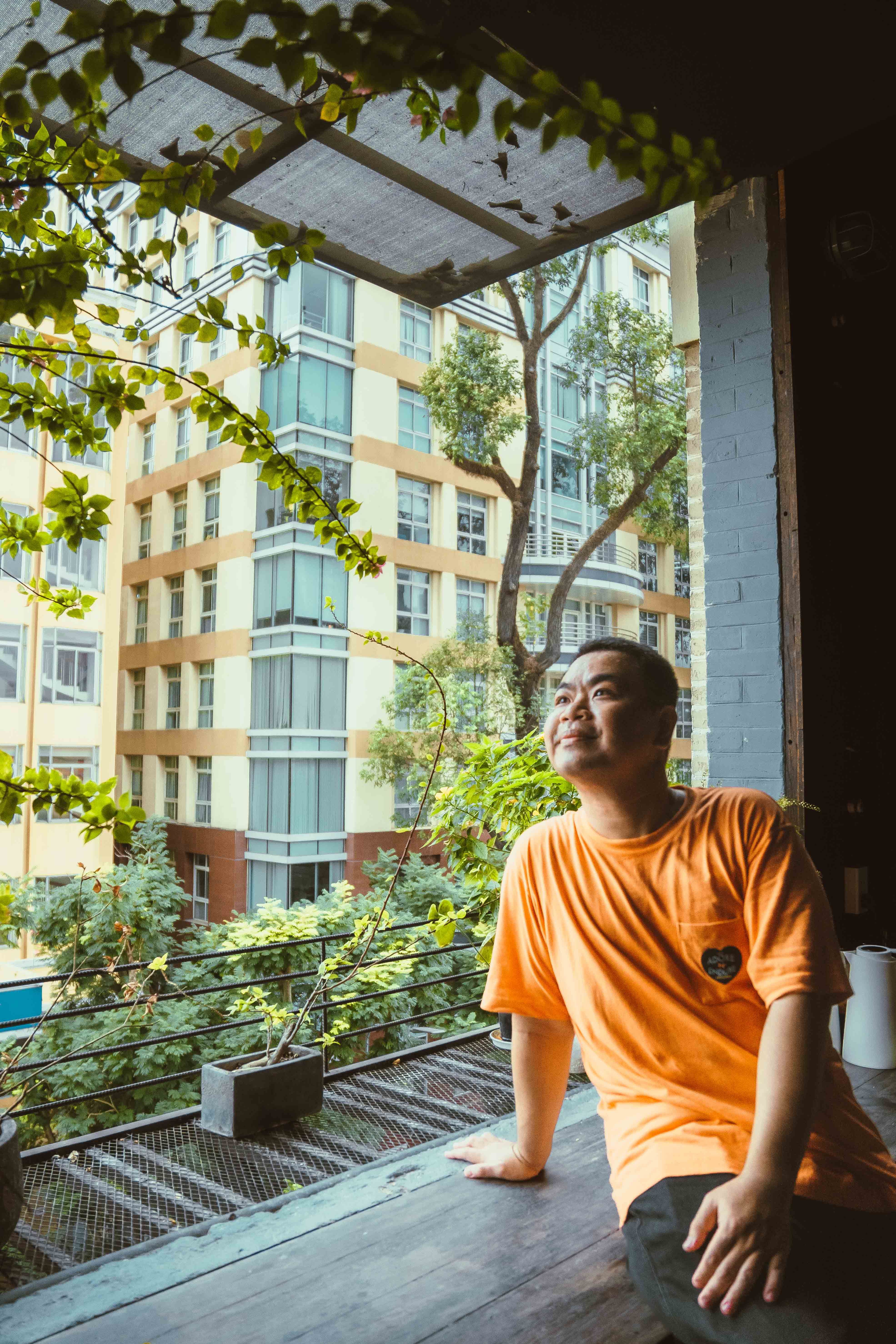 Man Sitting on Window Sill Overlooking Balcony with Plants in City ...