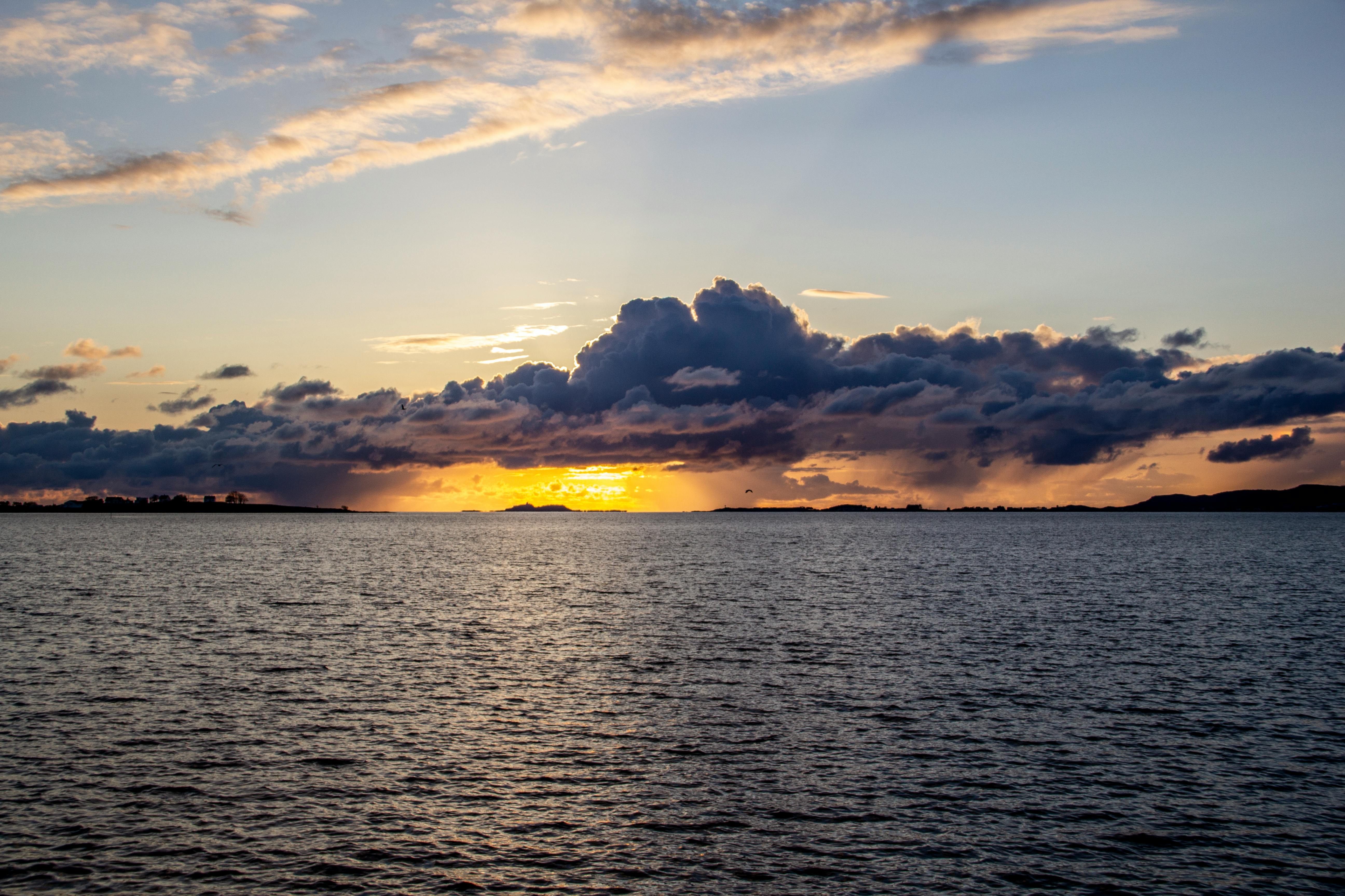 A sunset over the water with clouds in the sky · Free Stock Photo