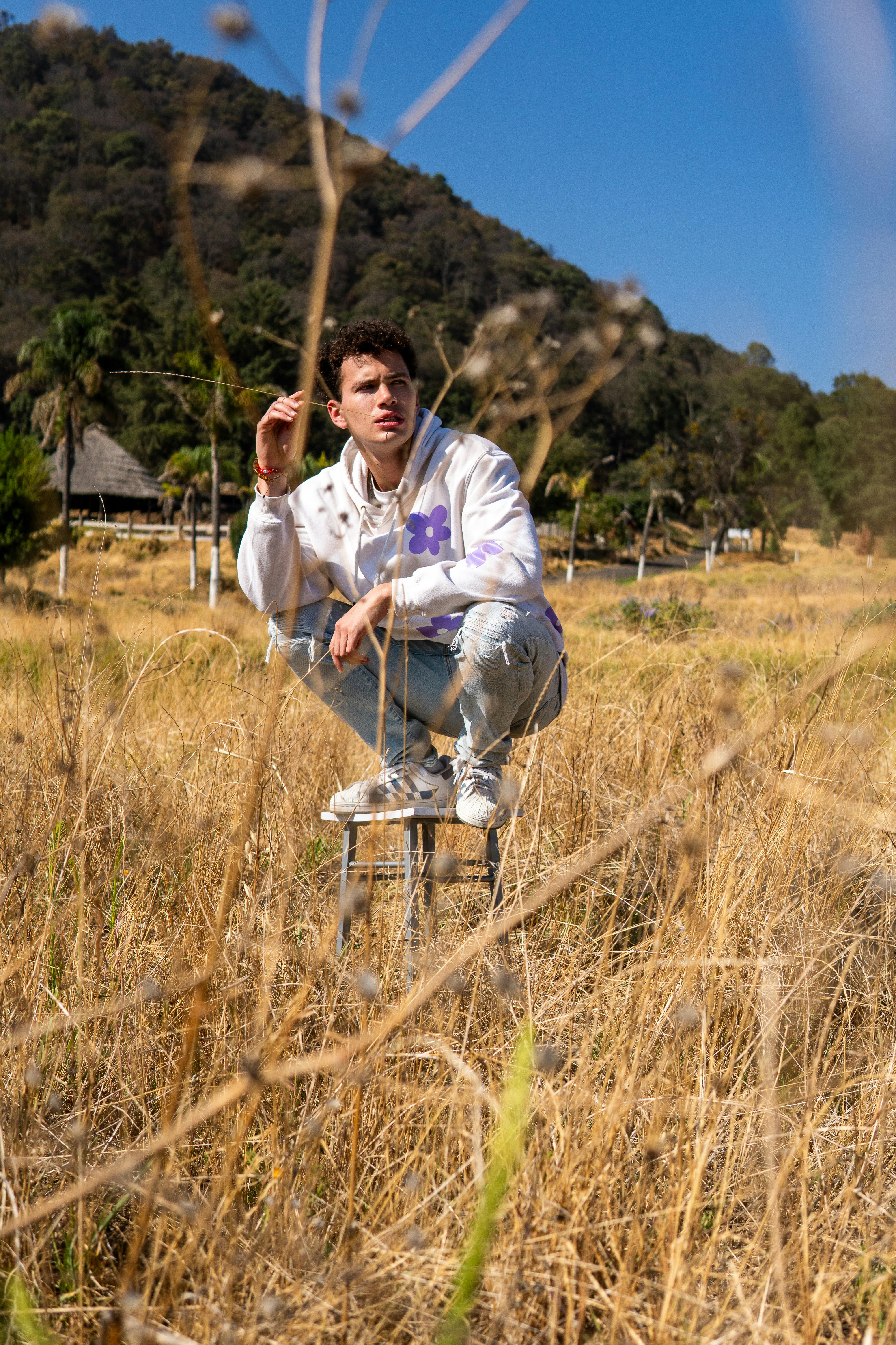 A Young Man Crouching on a Chair on the Field · Free Stock Photo