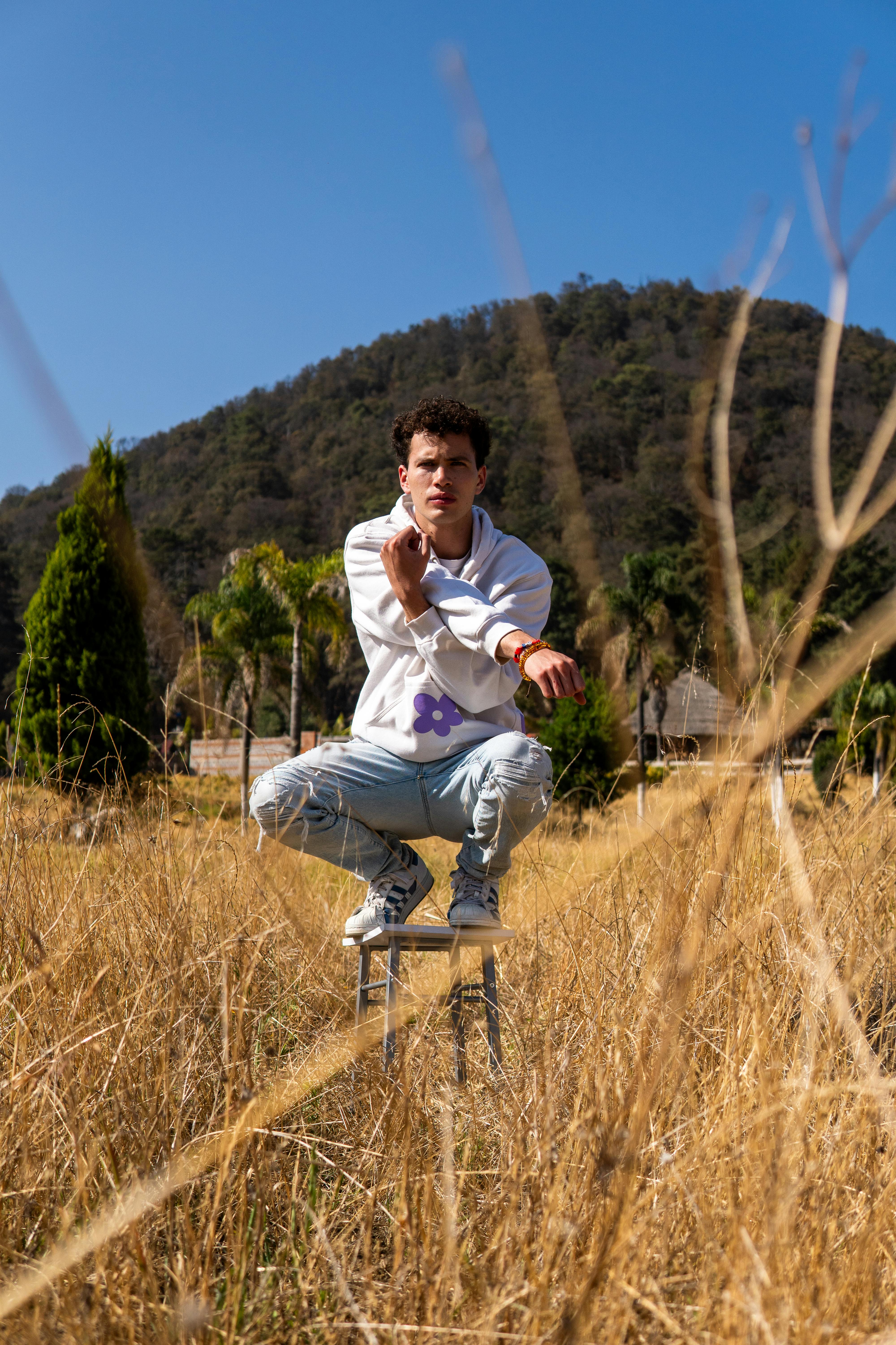 A Young Man Crouching on a Chair on the Field · Free Stock Photo
