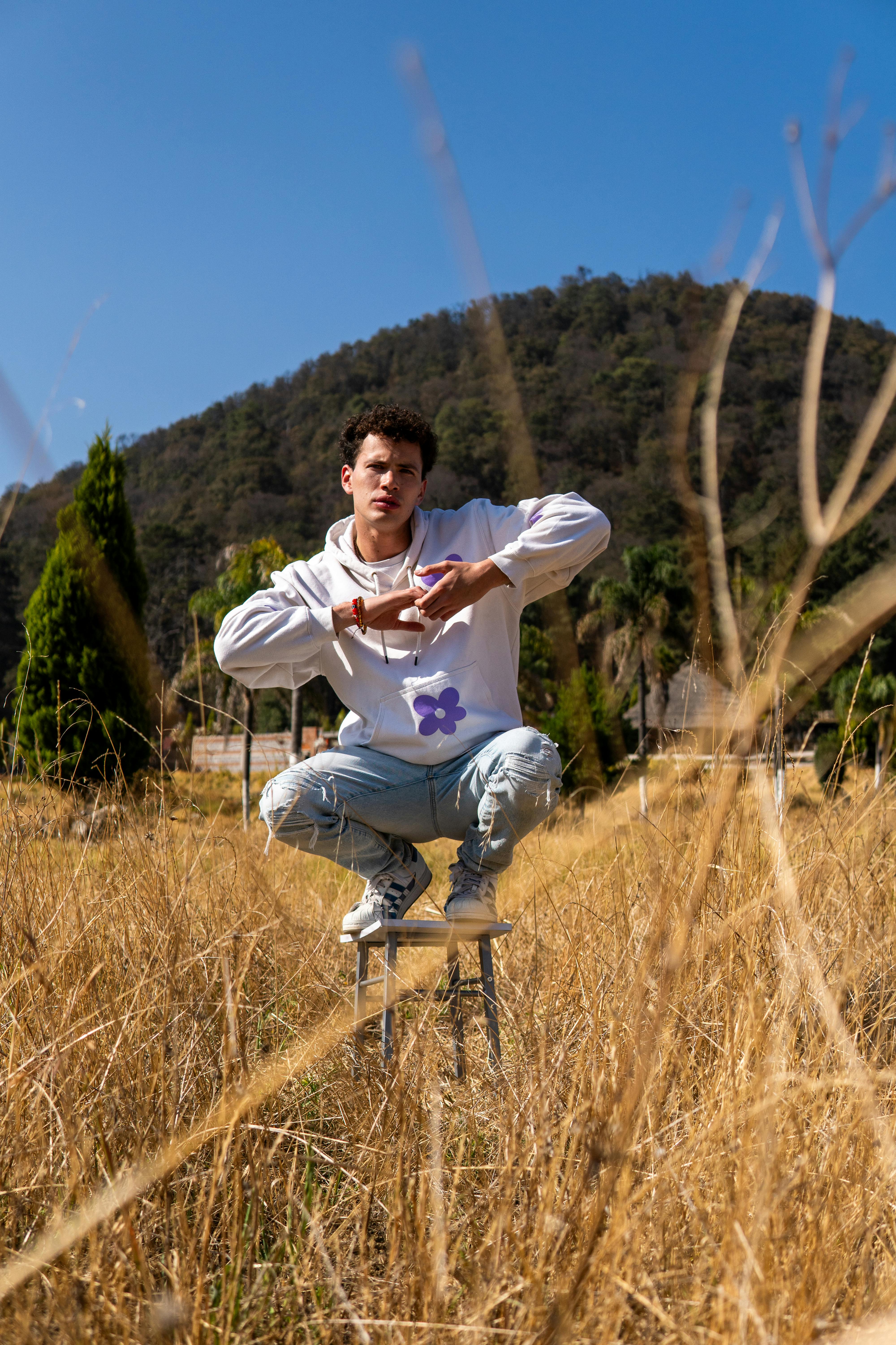 A Young Man Crouching on a Chair on the Field · Free Stock Photo