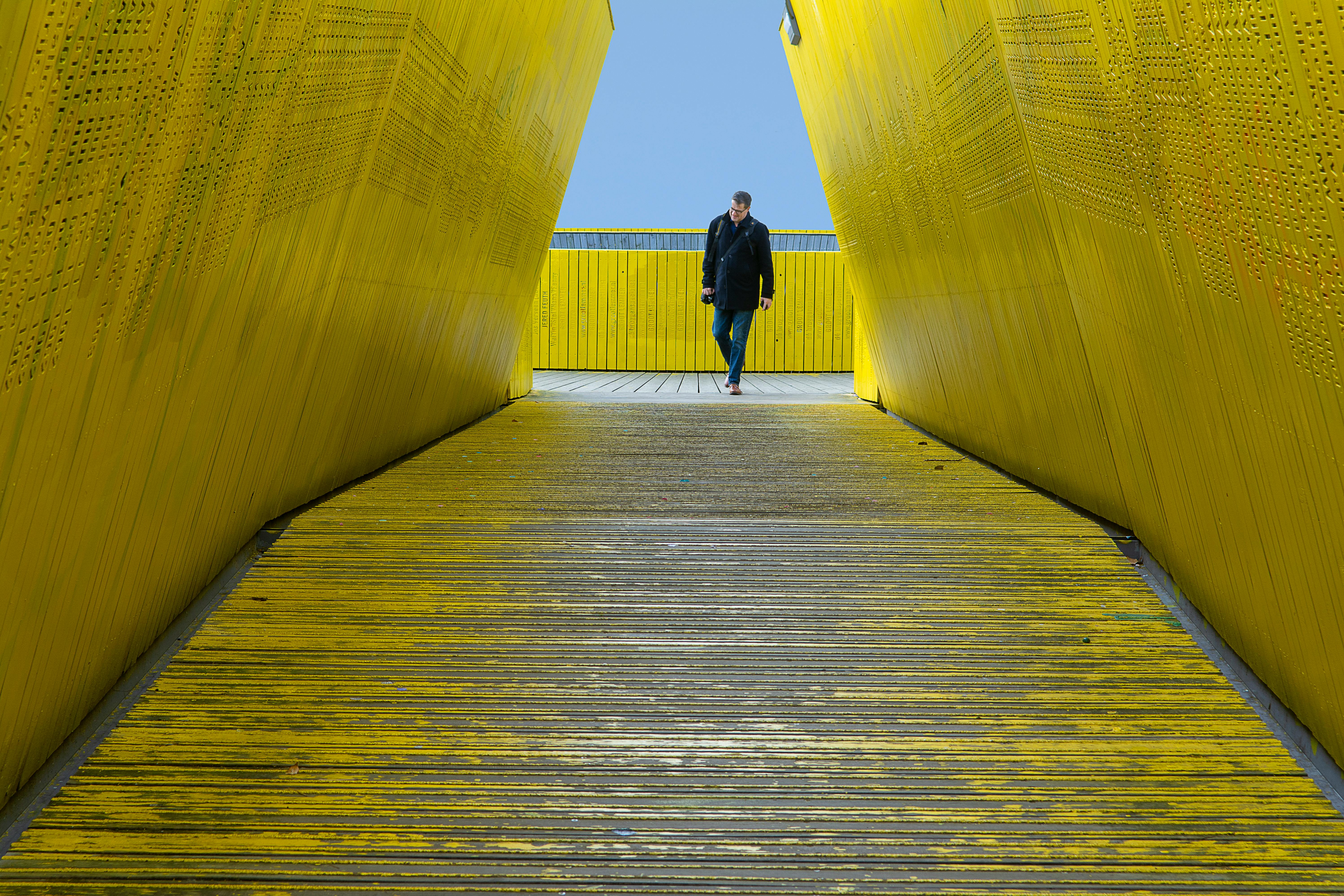 A person walking down a yellow walkway with a blue sky · Free Stock Photo