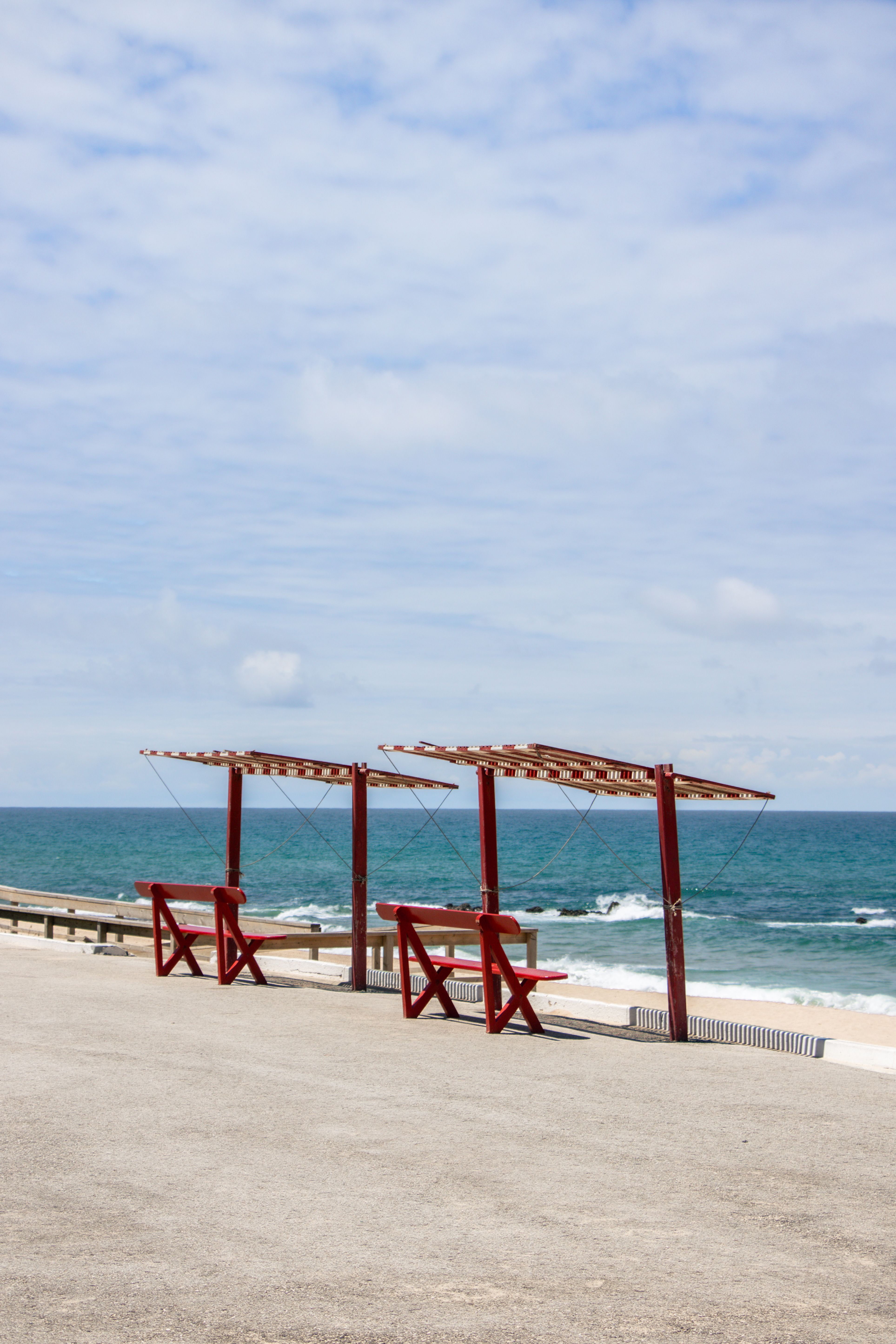 Two red benches sit on the beach near the ocean · Free Stock Photo