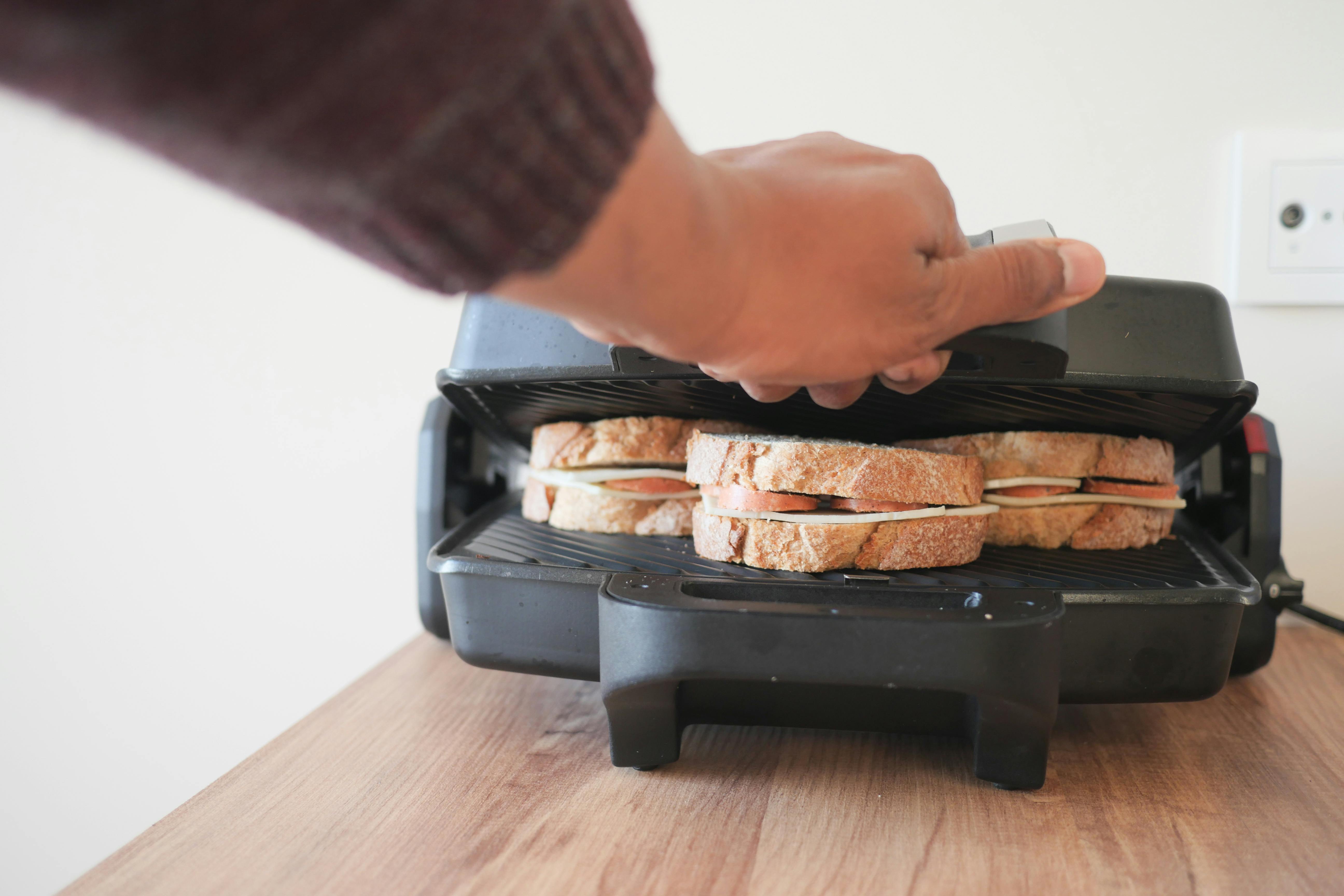 A person is holding a sandwich in a toaster · Free Stock Photo