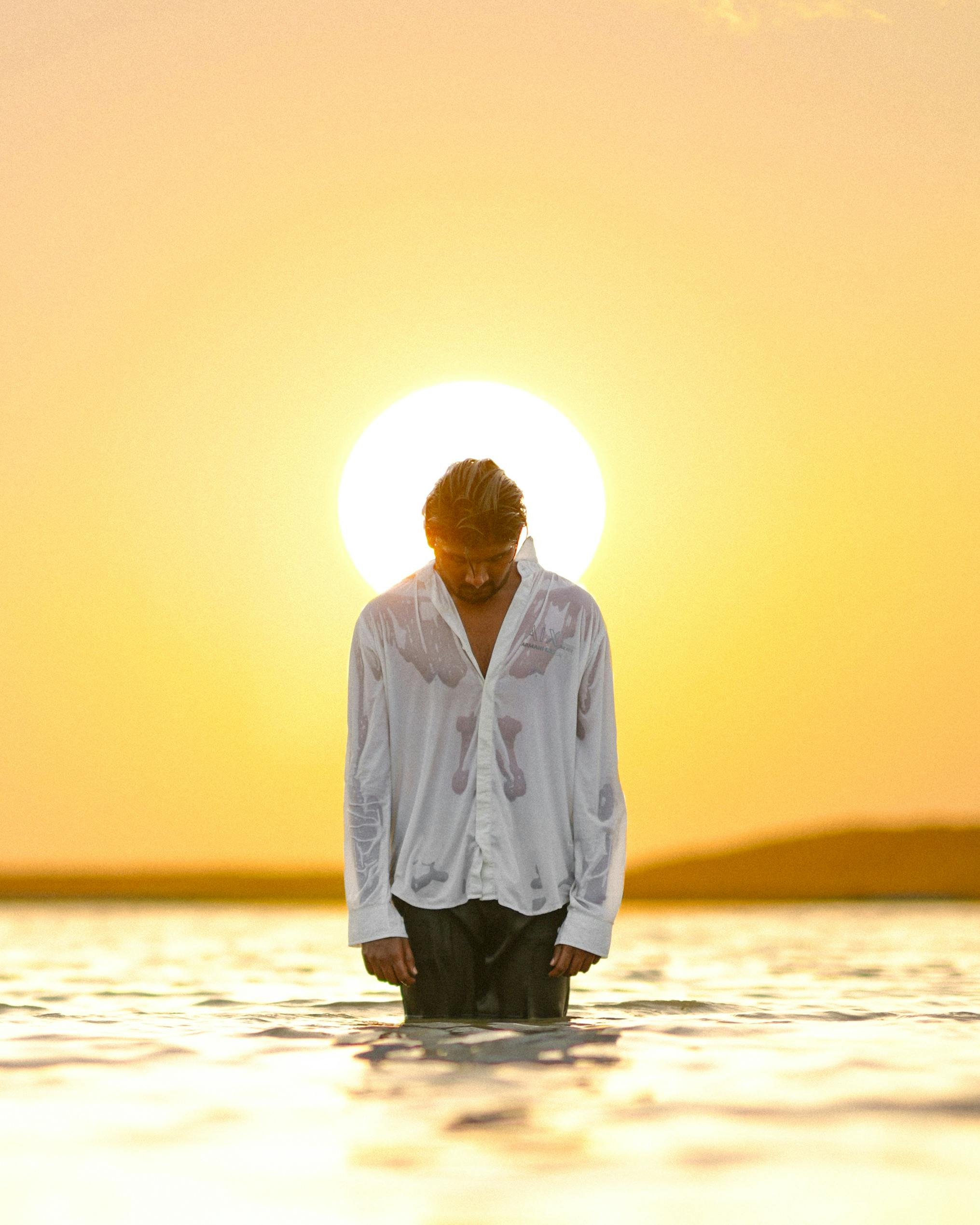 Man Standing Knee-Deep in Water against the Setting Sun · Free Stock Photo