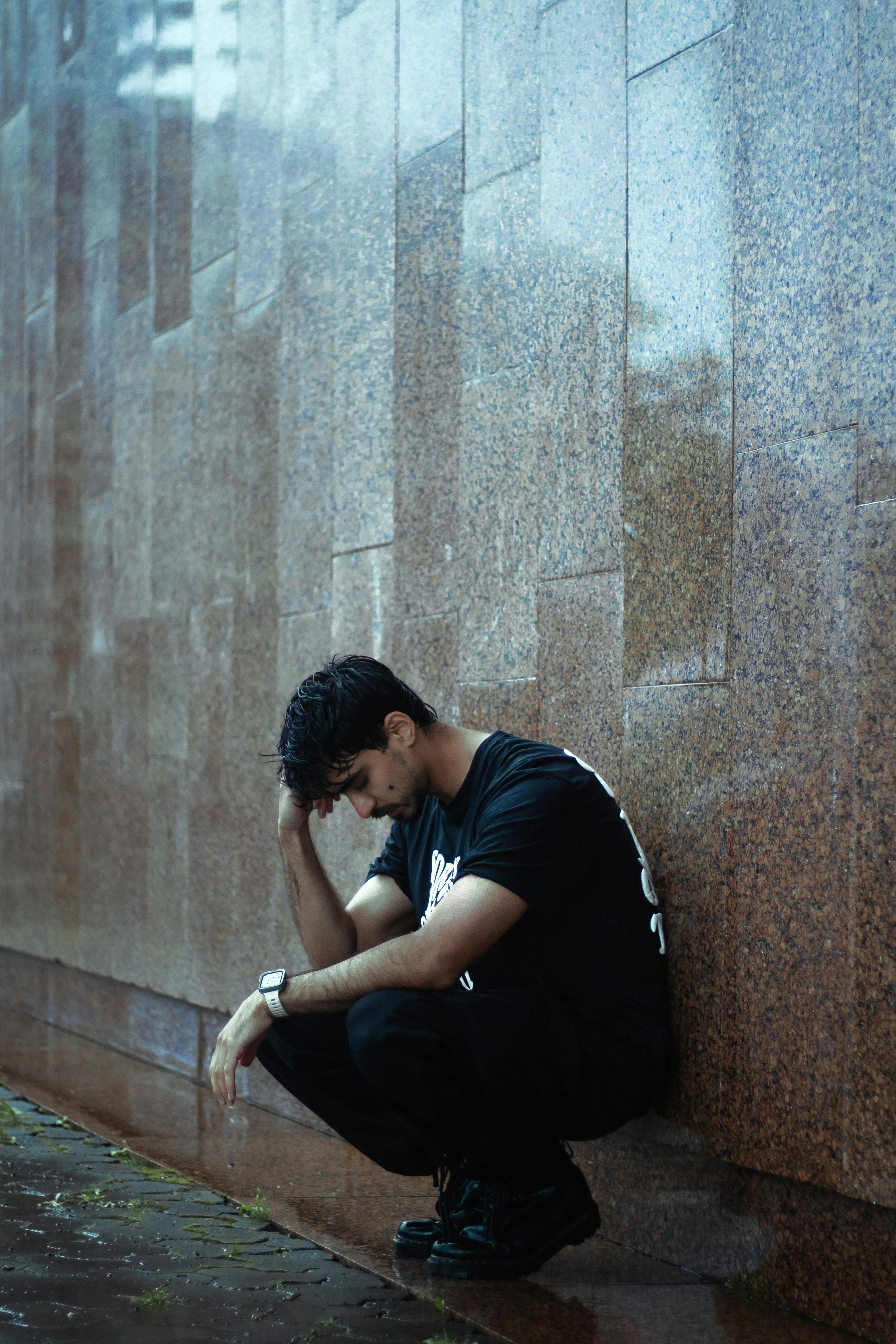 A man crouching down in front of a wall · Free Stock Photo