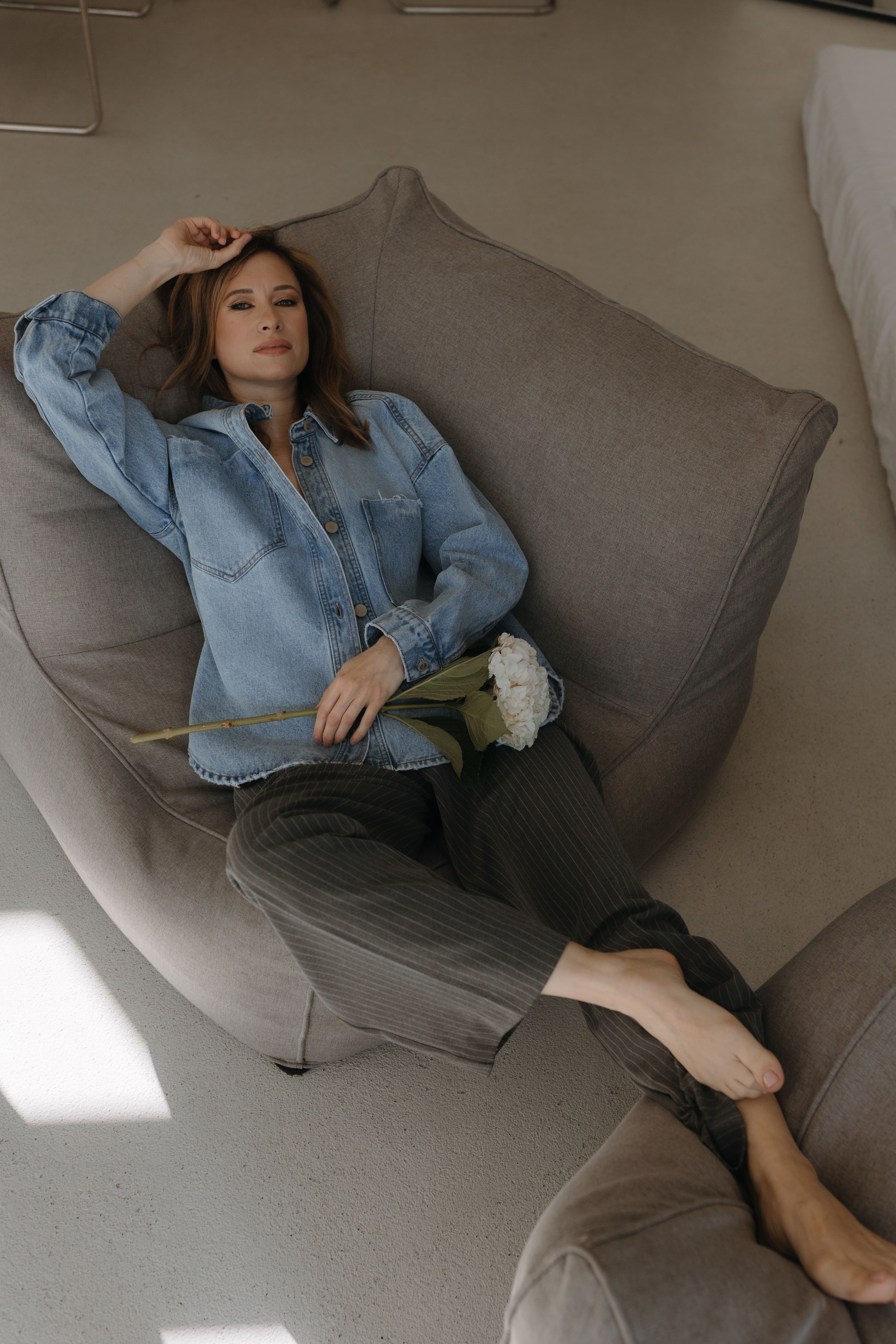 Barefoot Woman in Denim Shirt with Flower Lying on Gray Sofa · Free ...