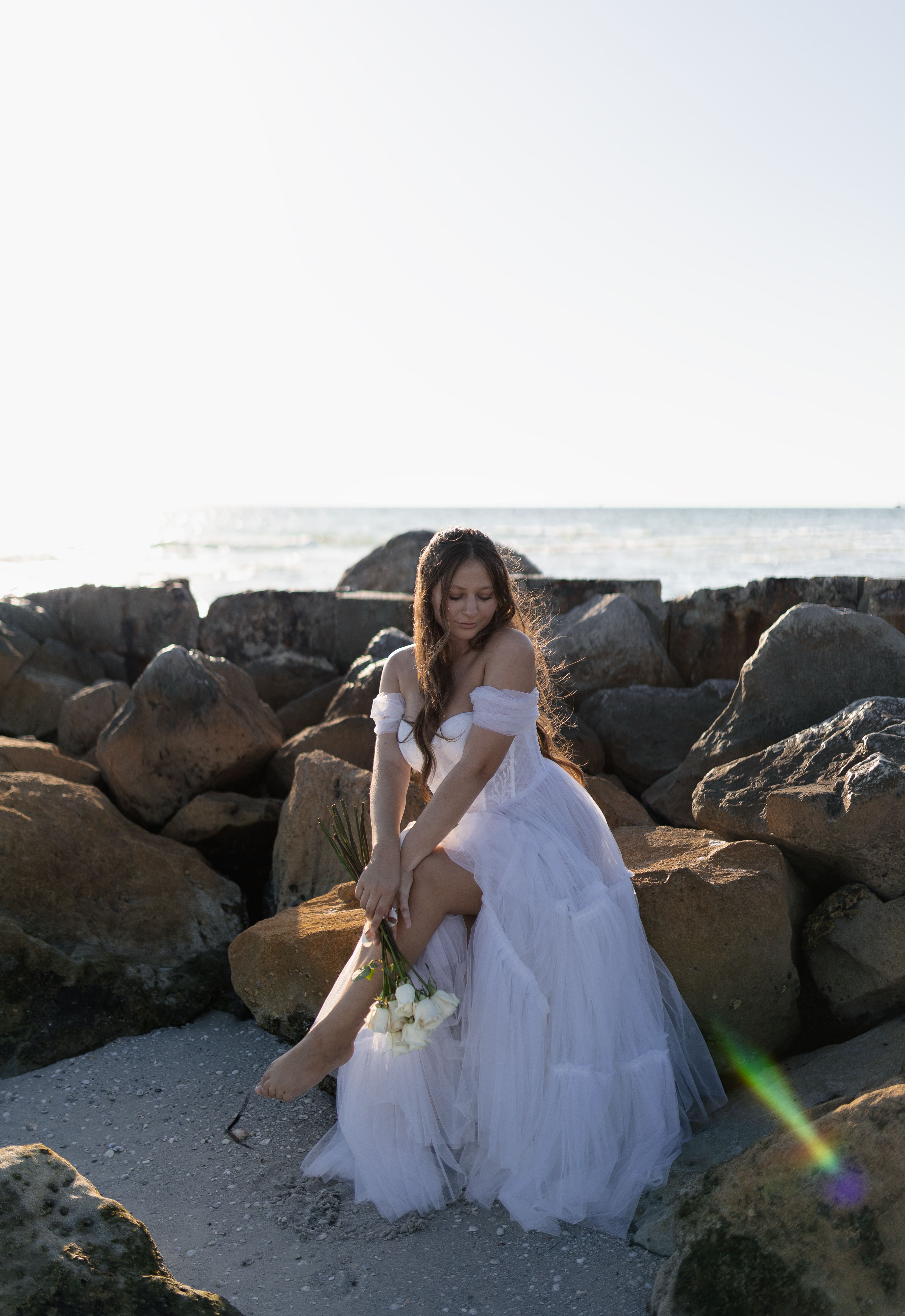 Bride Sitting in Wedding Dress on Rocks on Sea Shore · Free Stock Photo