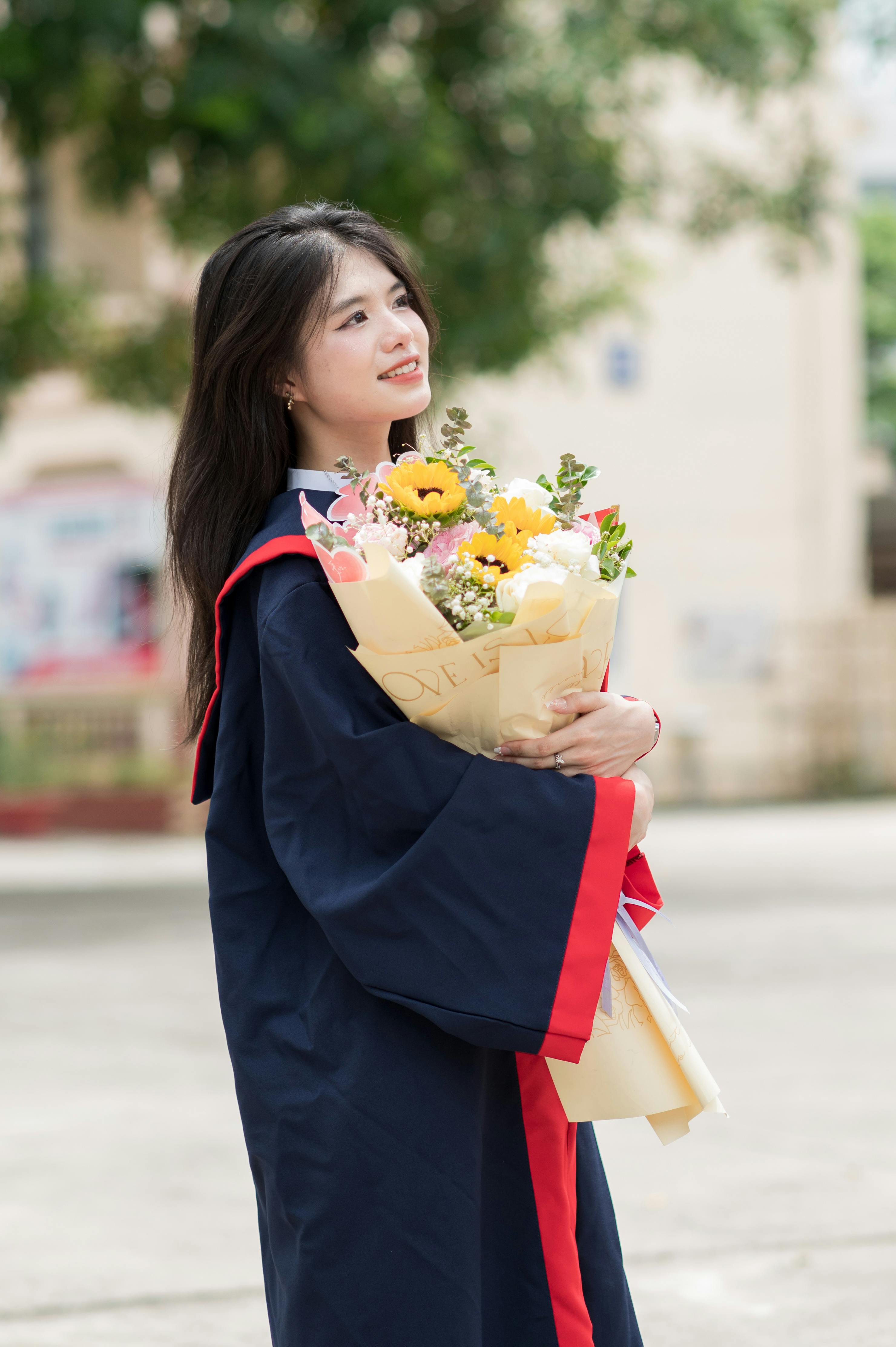 A woman in a graduation gown holding flowers · Free Stock Photo
