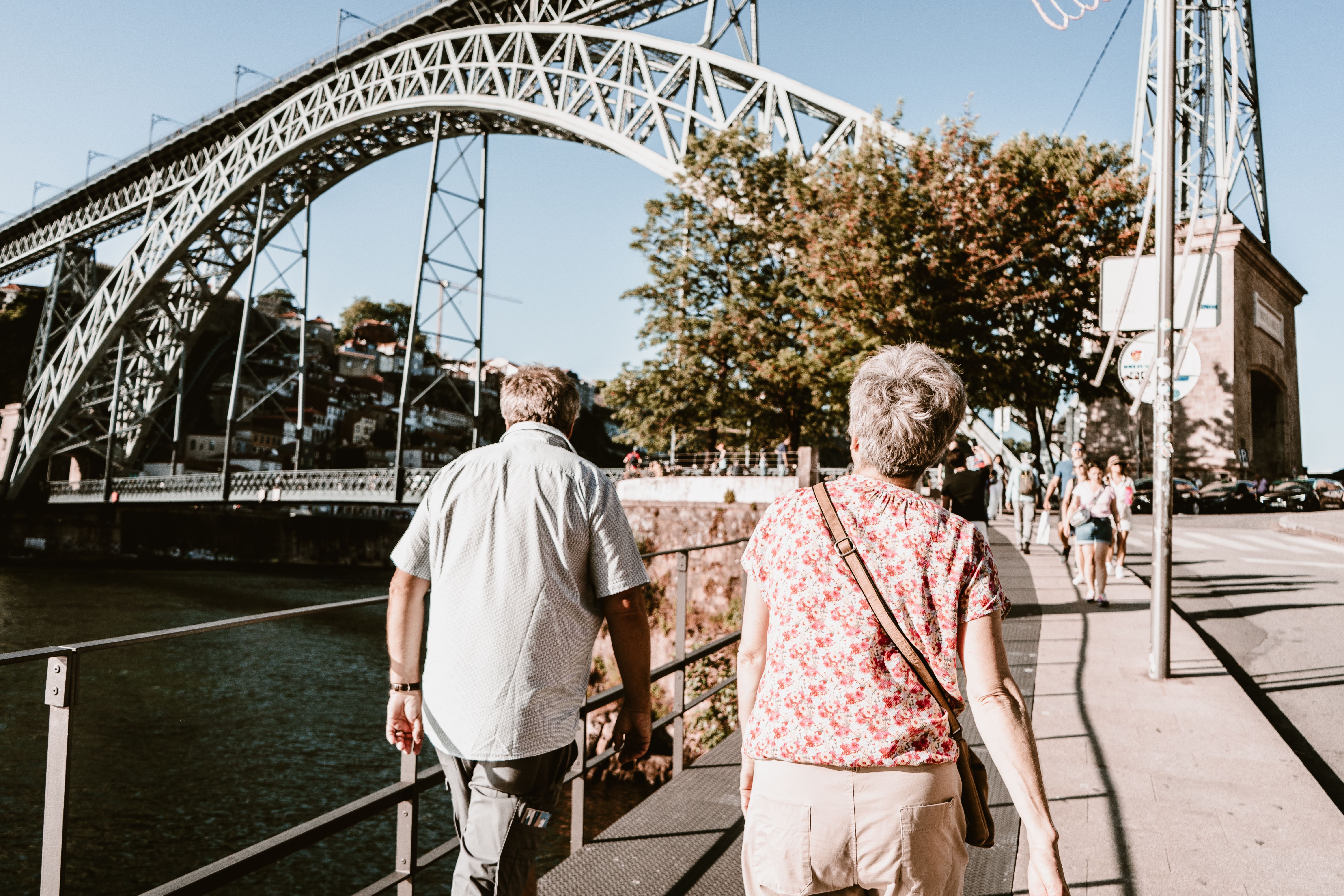 Two people walking along a river with a bridge in the background · Free ...