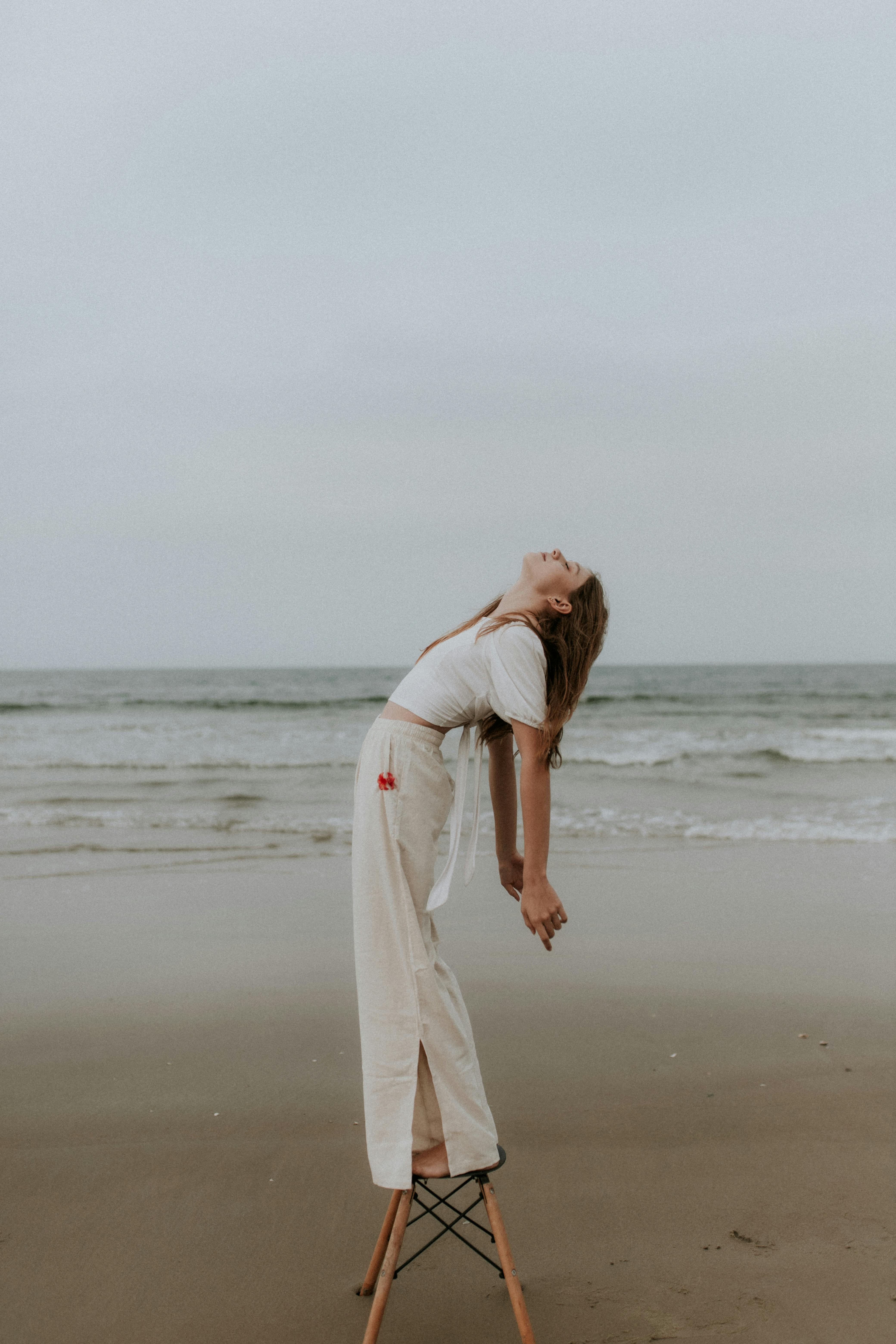 Woman Standing and Bending on Chair on Seashore · Free Stock Photo