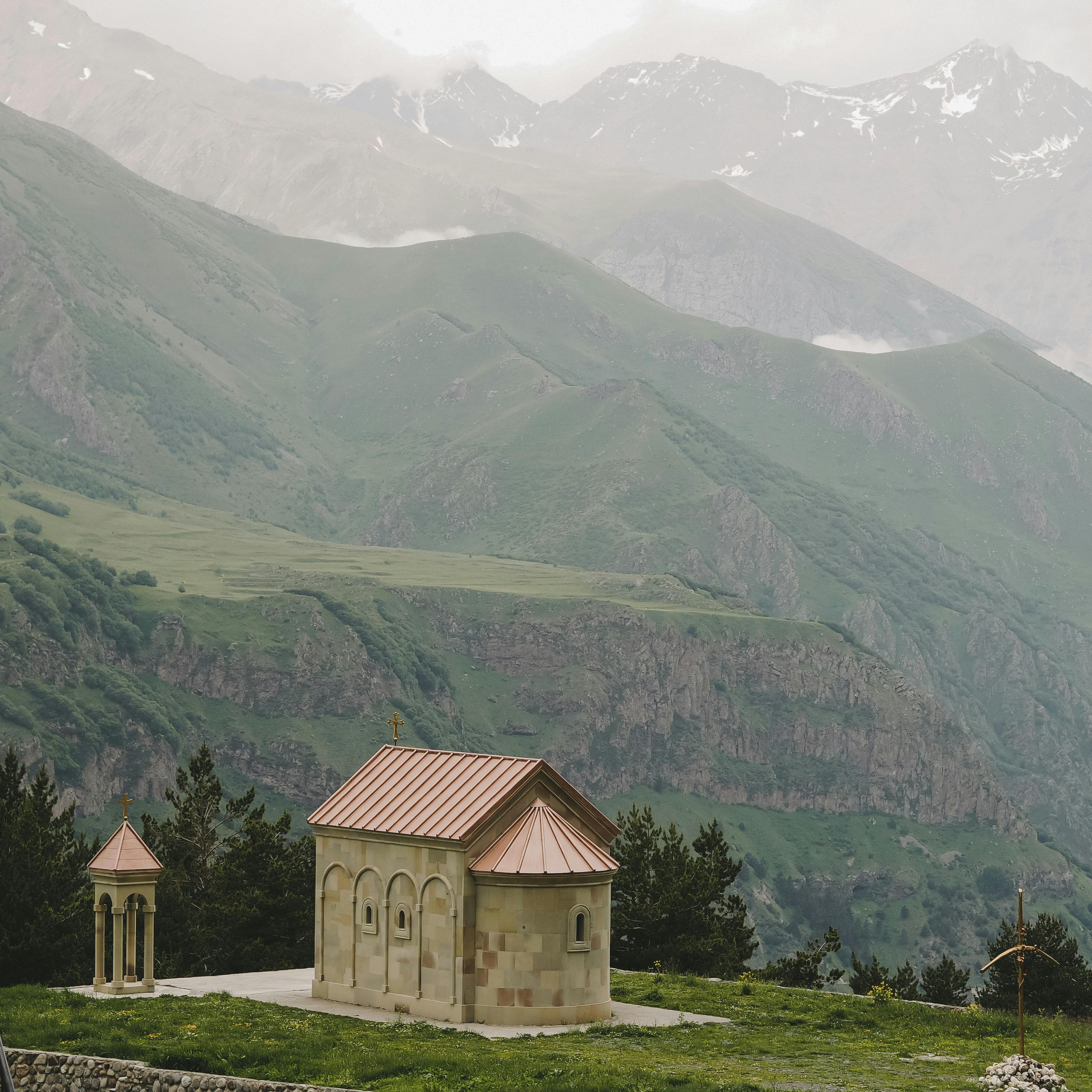 Medieval church on grassy hilltop surrounded by majestic mountains ...