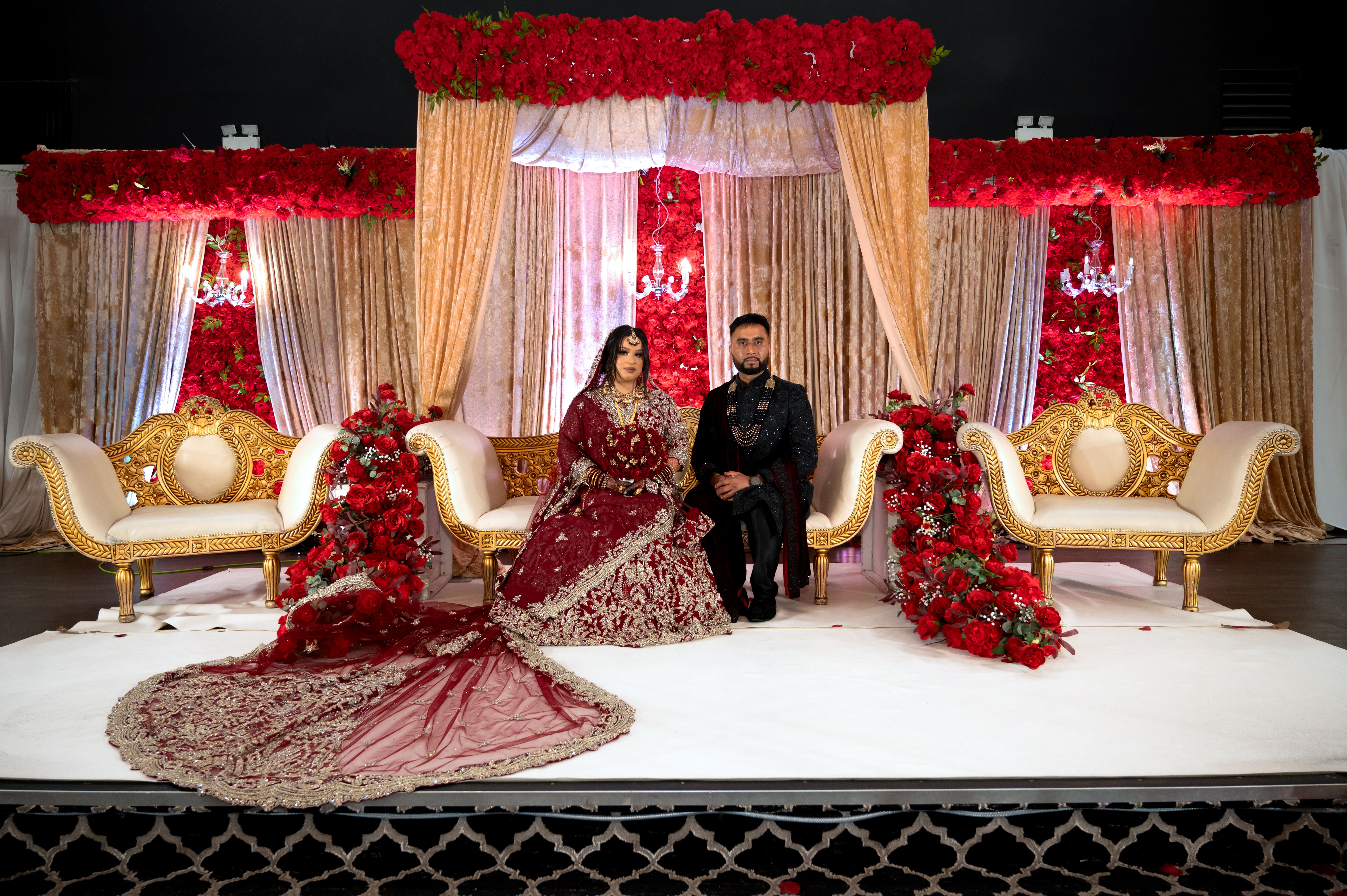A couple sitting on a stage in front of a red and gold backdrop · Free ...