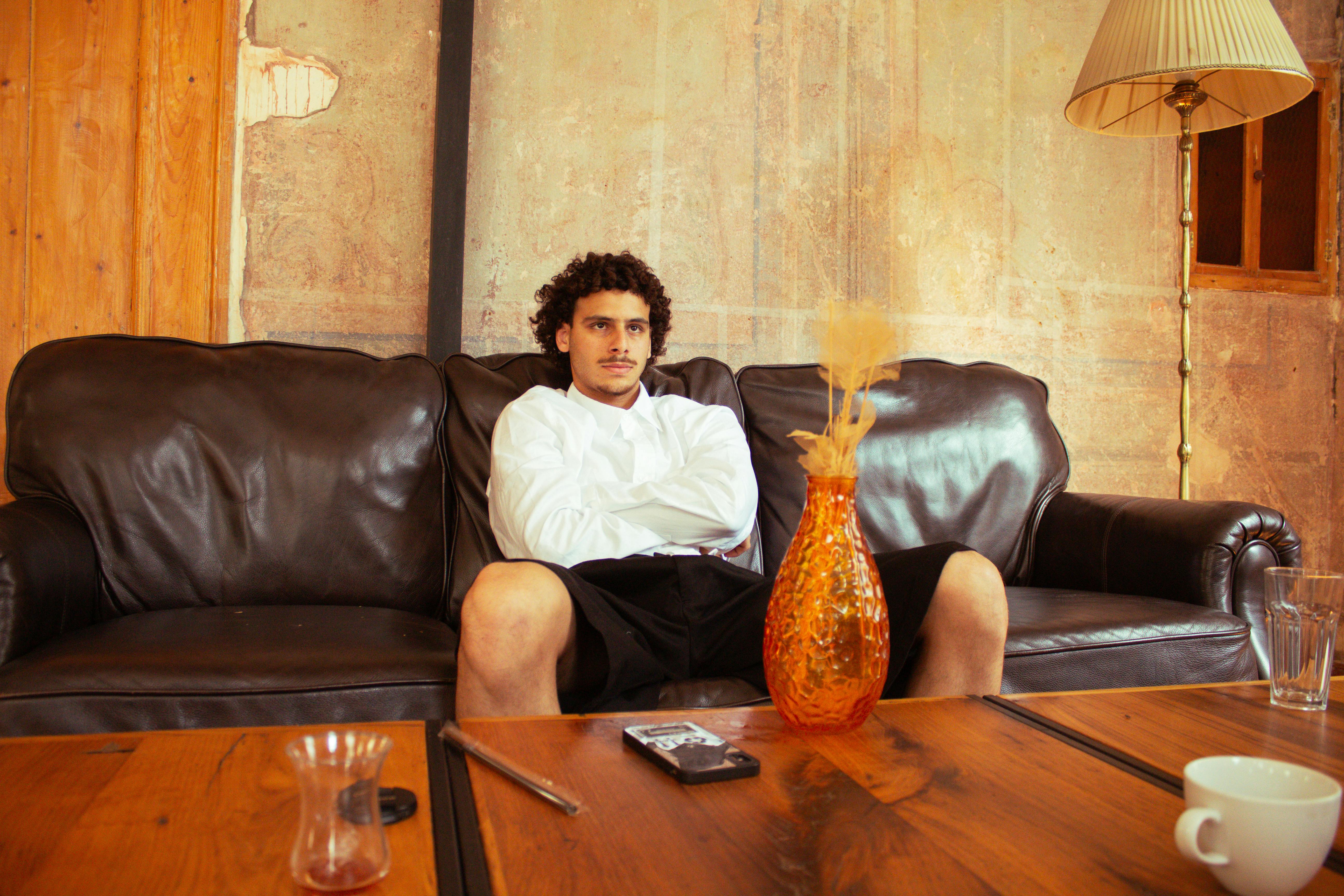 Young Man in White Shirt and Black Shorts Sitting on Black Sofa with ...