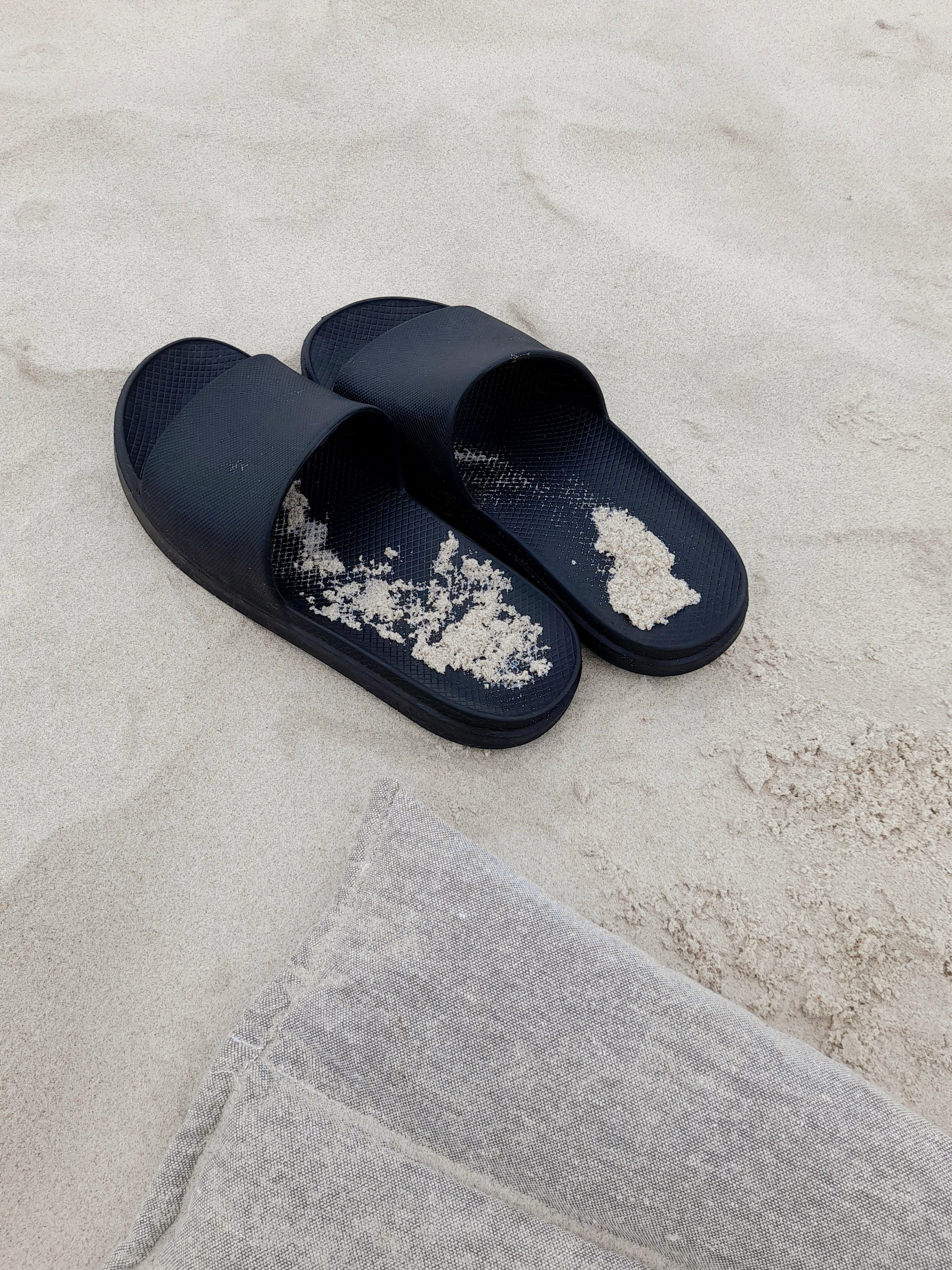 A pair of black slippers on the beach · Free Stock Photo