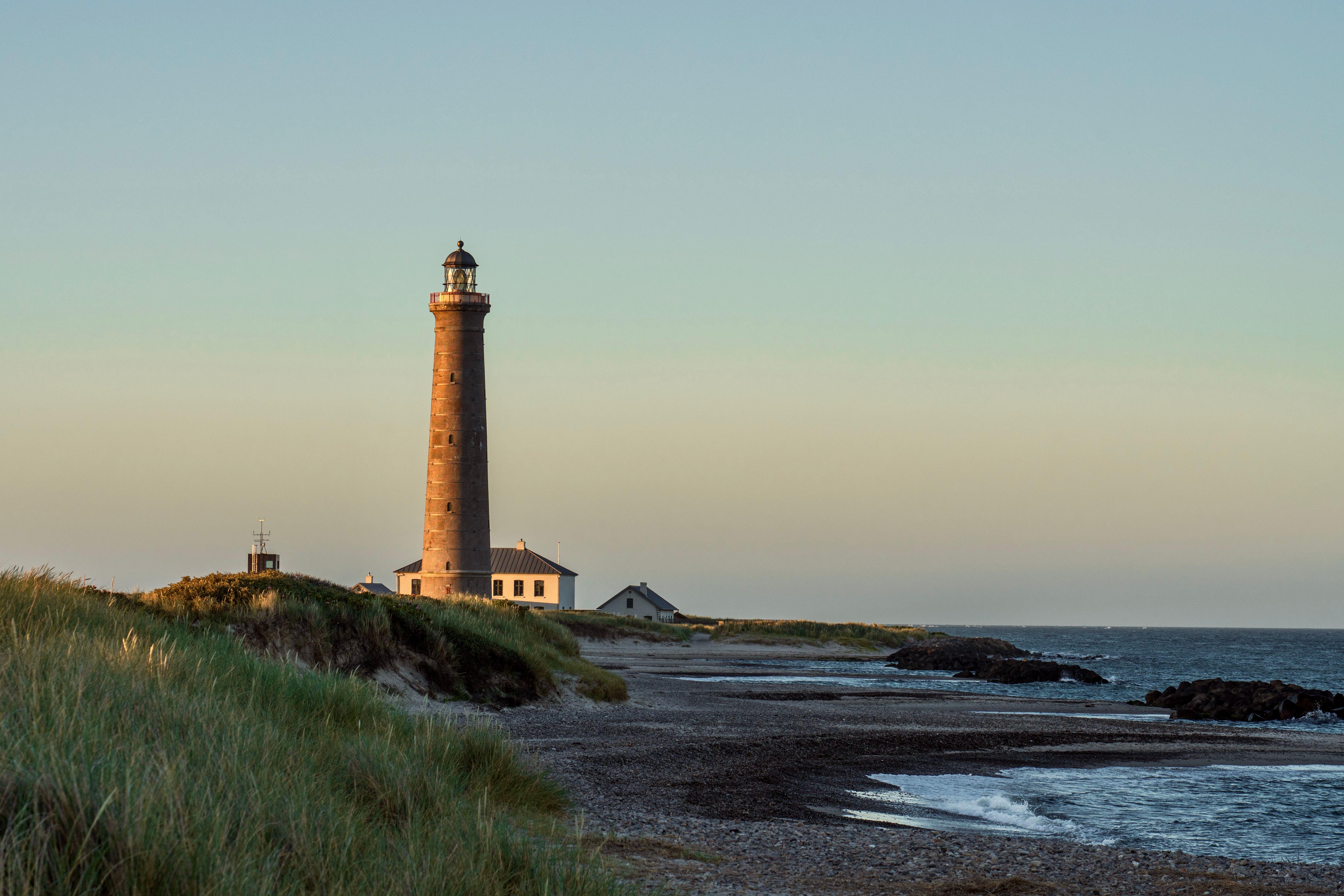 A lighthouse sits on a beach near the ocean · Free Stock Photo