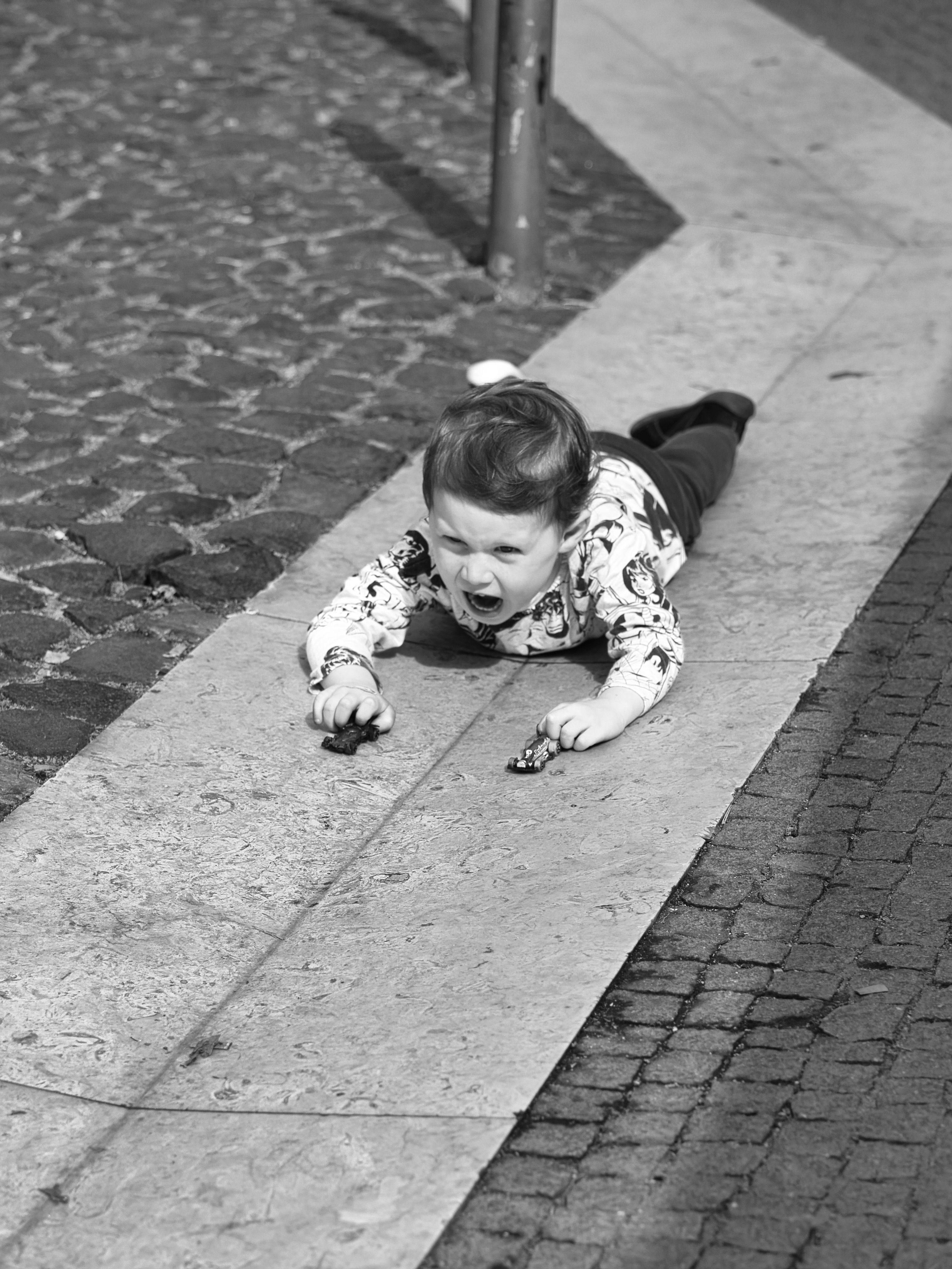 Child Lying Down with Toys on Pavement · Free Stock Photo
