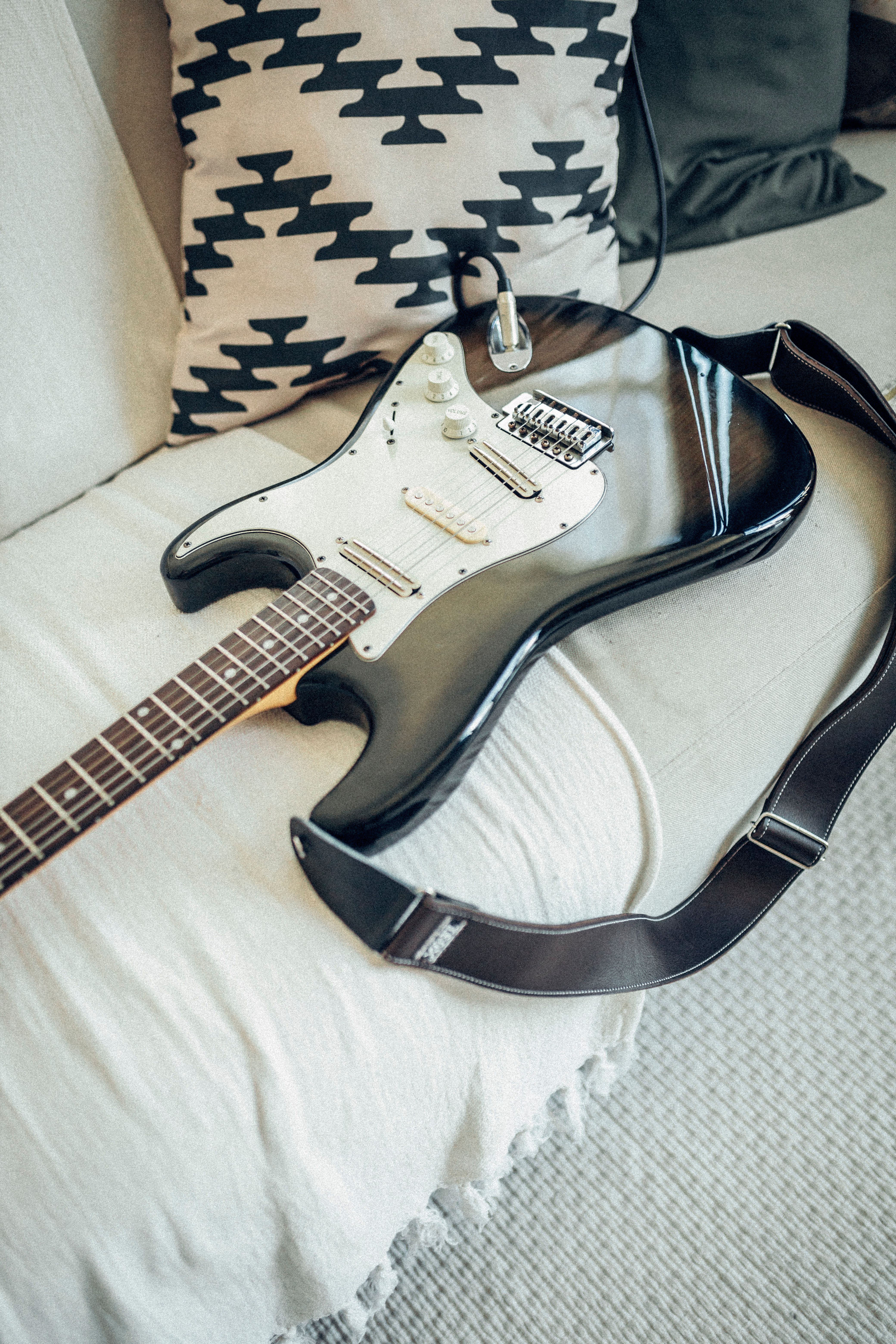 A guitar sits on a couch with a leather strap · Free Stock Photo