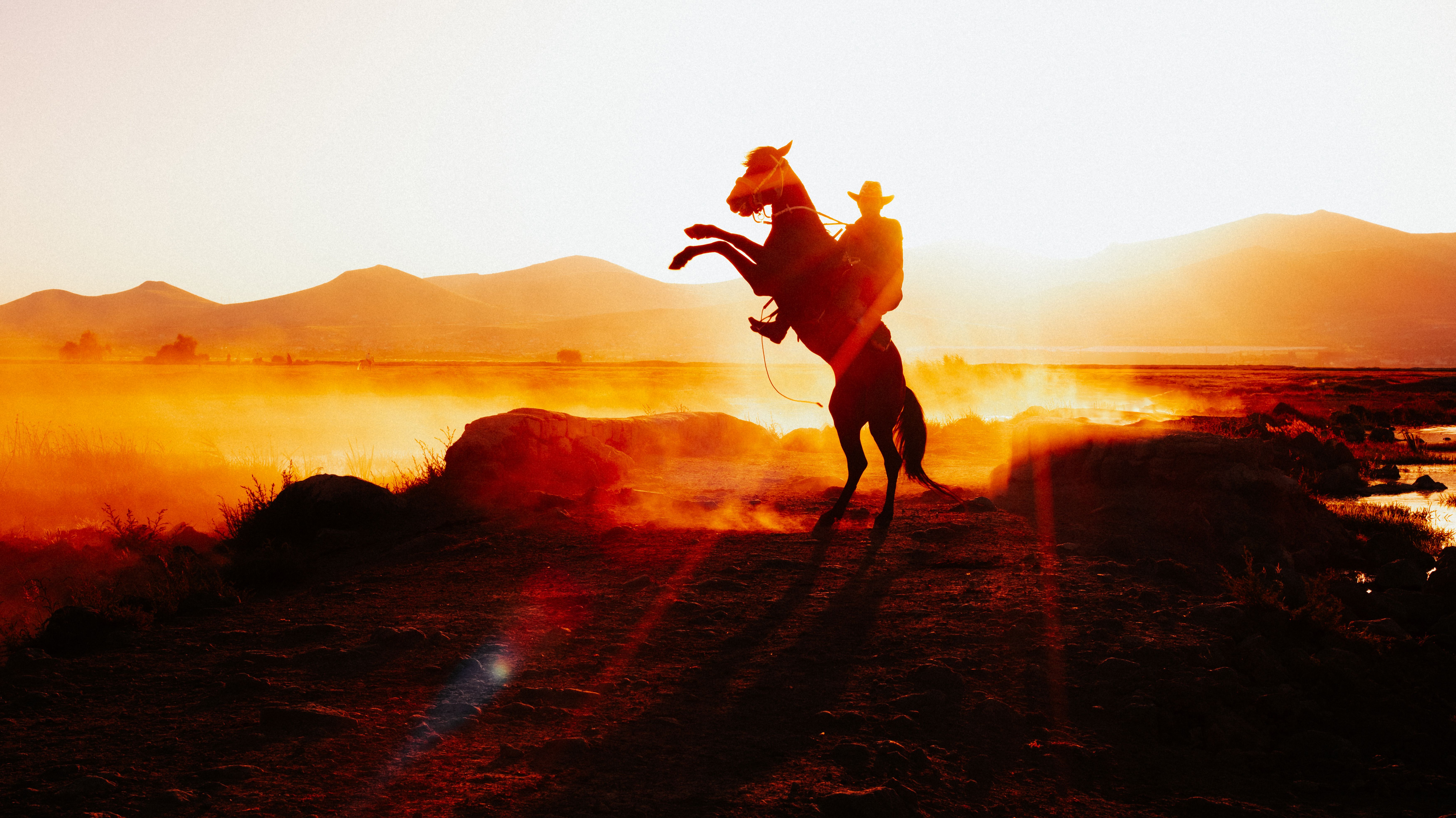 A cowboy is riding a horse at sunset · Free Stock Photo