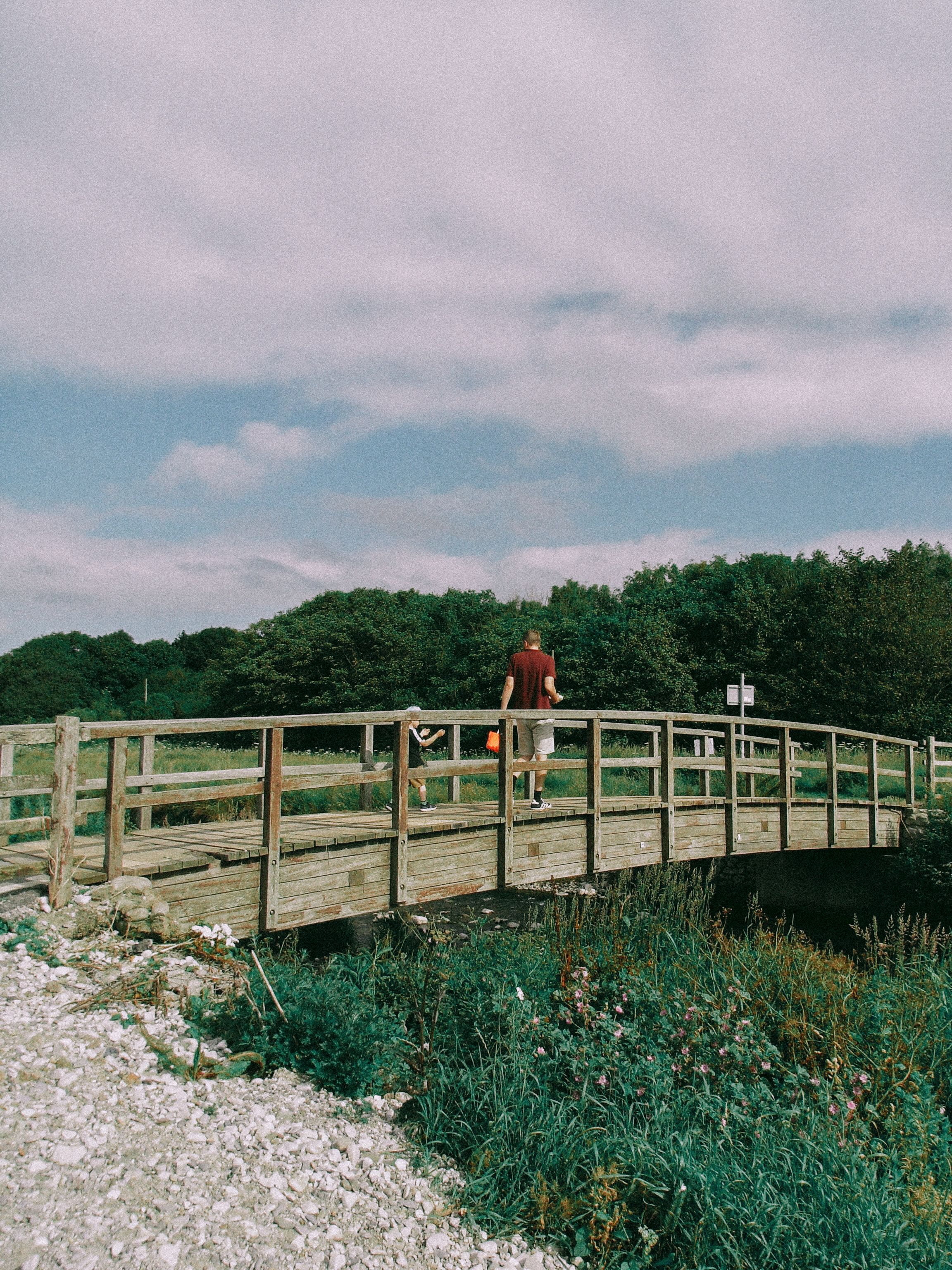 Man with Child Walking on Wooden Bridge over Small River · Free Stock Photo