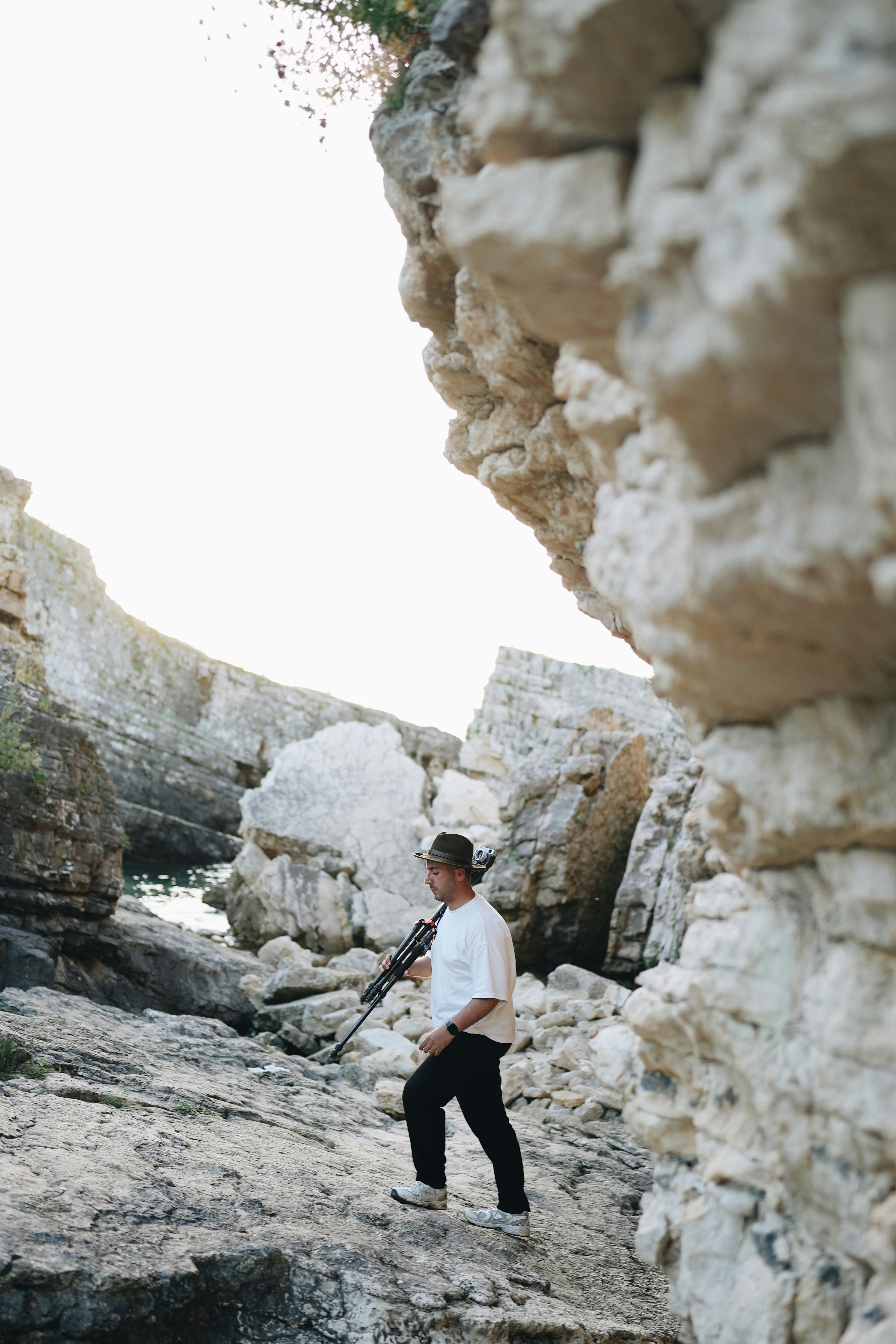 Man Holding Tripod Walking between Steep Rock Formations · Free Stock Photo