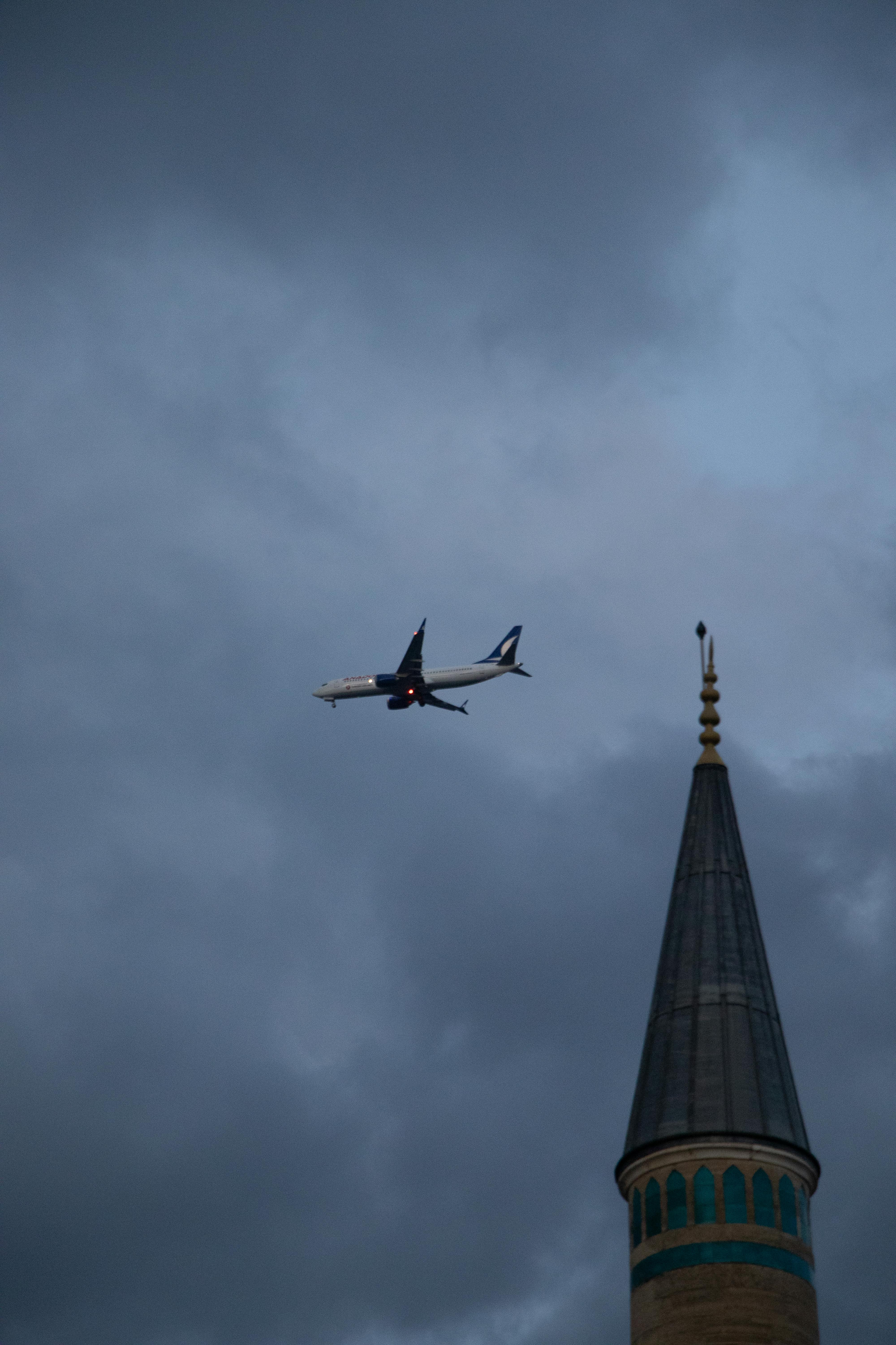 A plane flying over a mosque and a clock tower · Free Stock Photo
