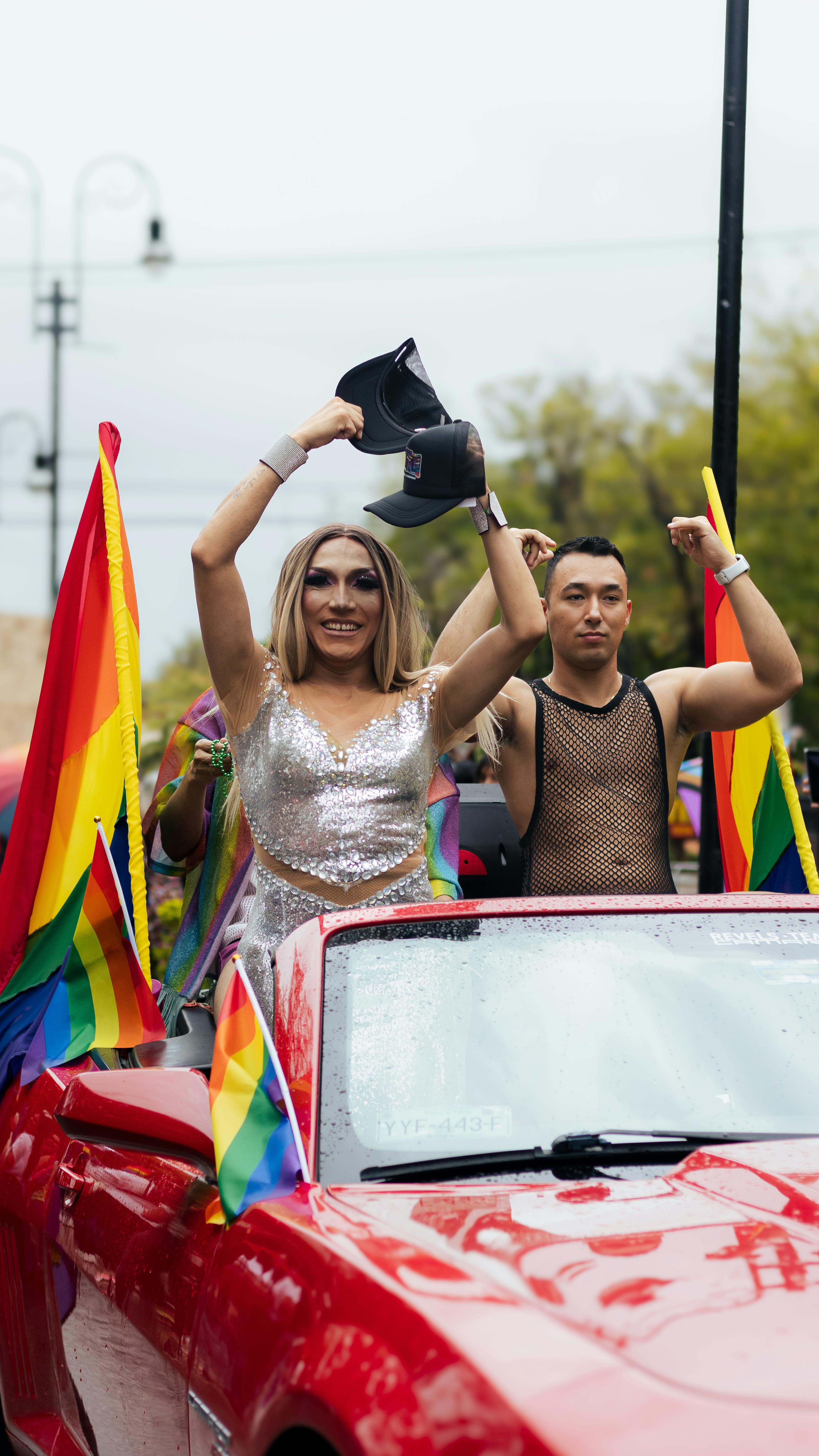 Two women in a convertible waving at a pride parade · Free Stock Photo