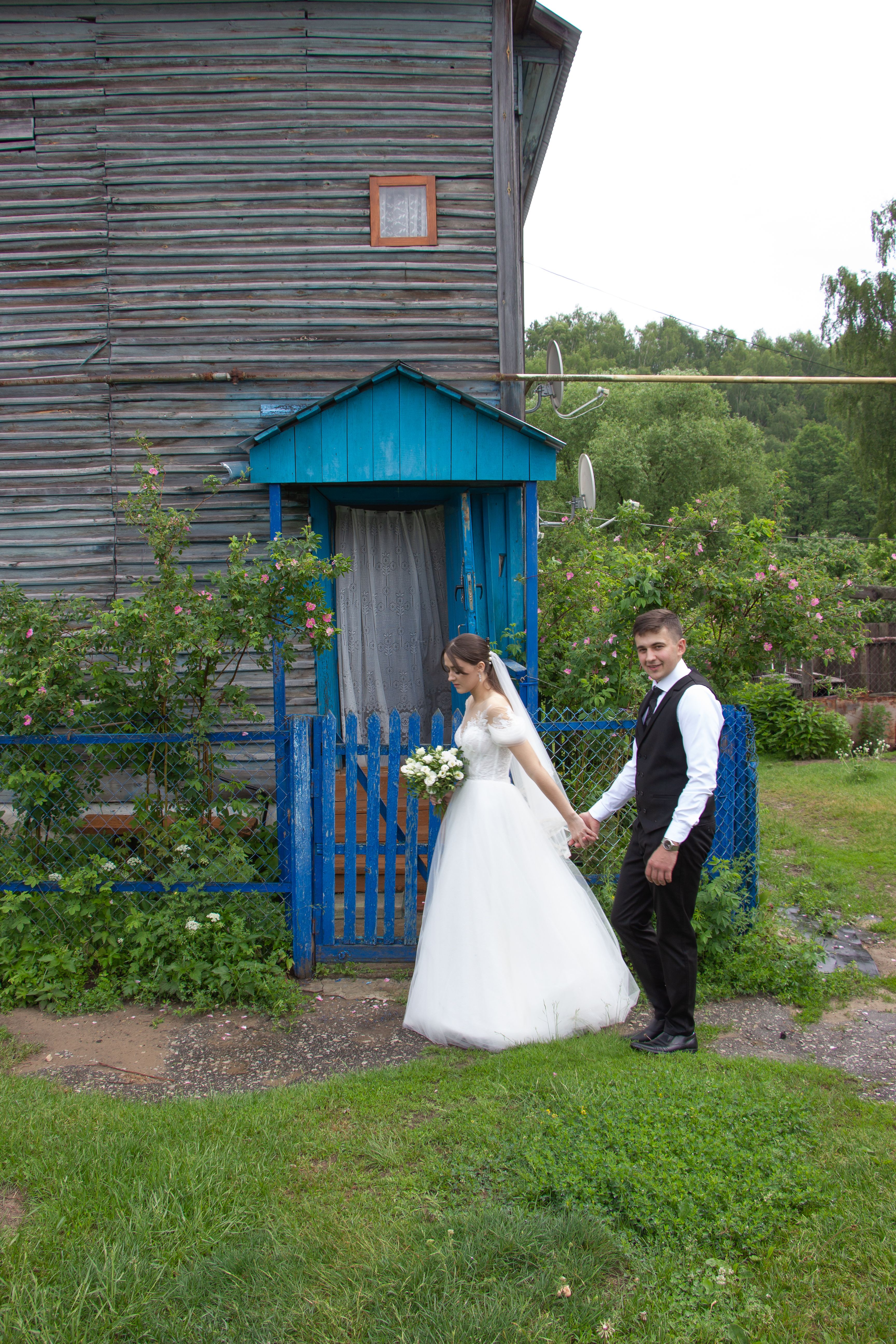 A bride and groom standing in front of a blue house · Free Stock Photo