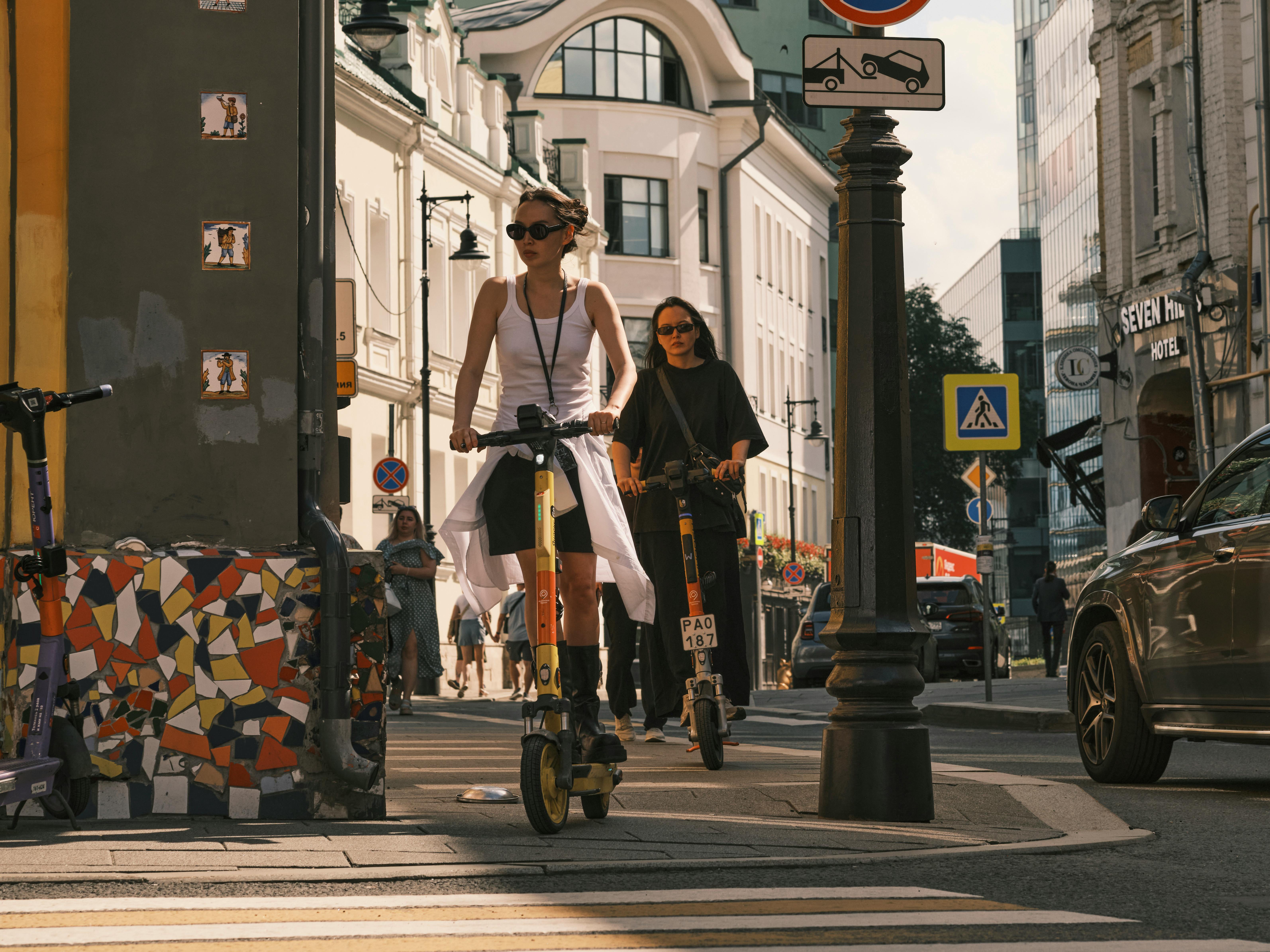 Women Riding Electric Scooters on City Sidewalk · Free Stock Photo