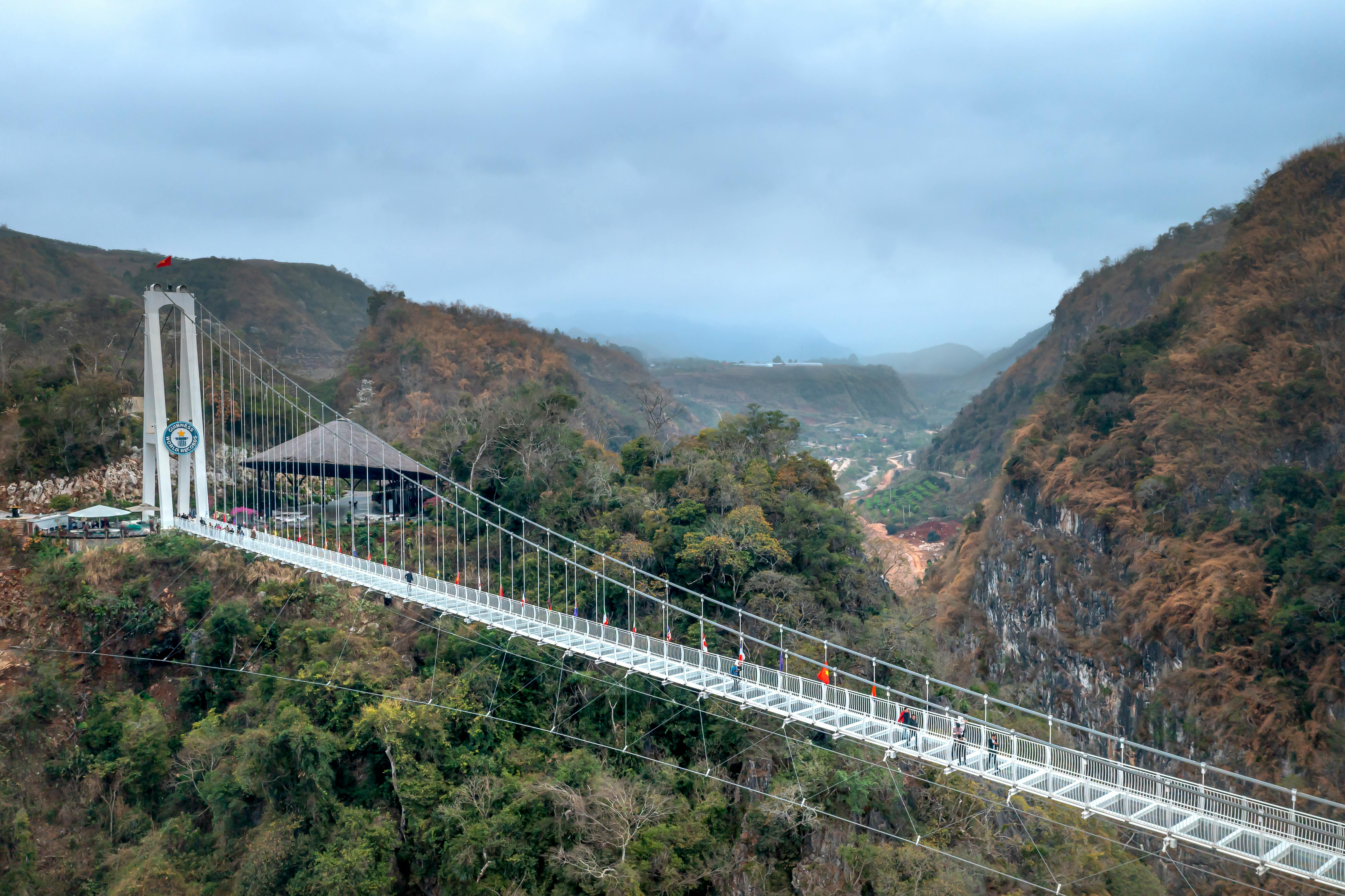 A suspension bridge over a valley with mountains in the background ...