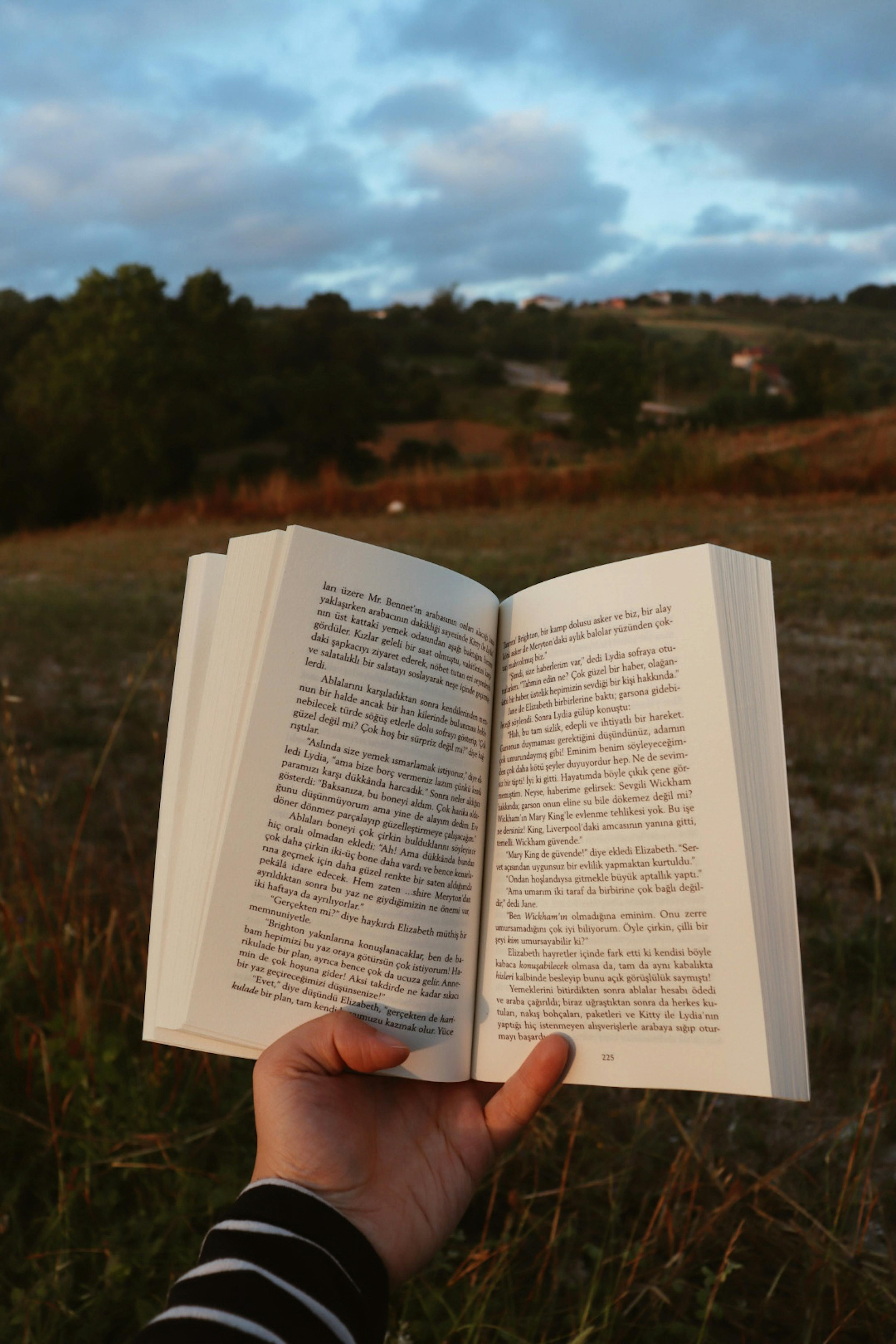 Person Reading Open Book Sitting on Grassland Field on Hill on Evening ...