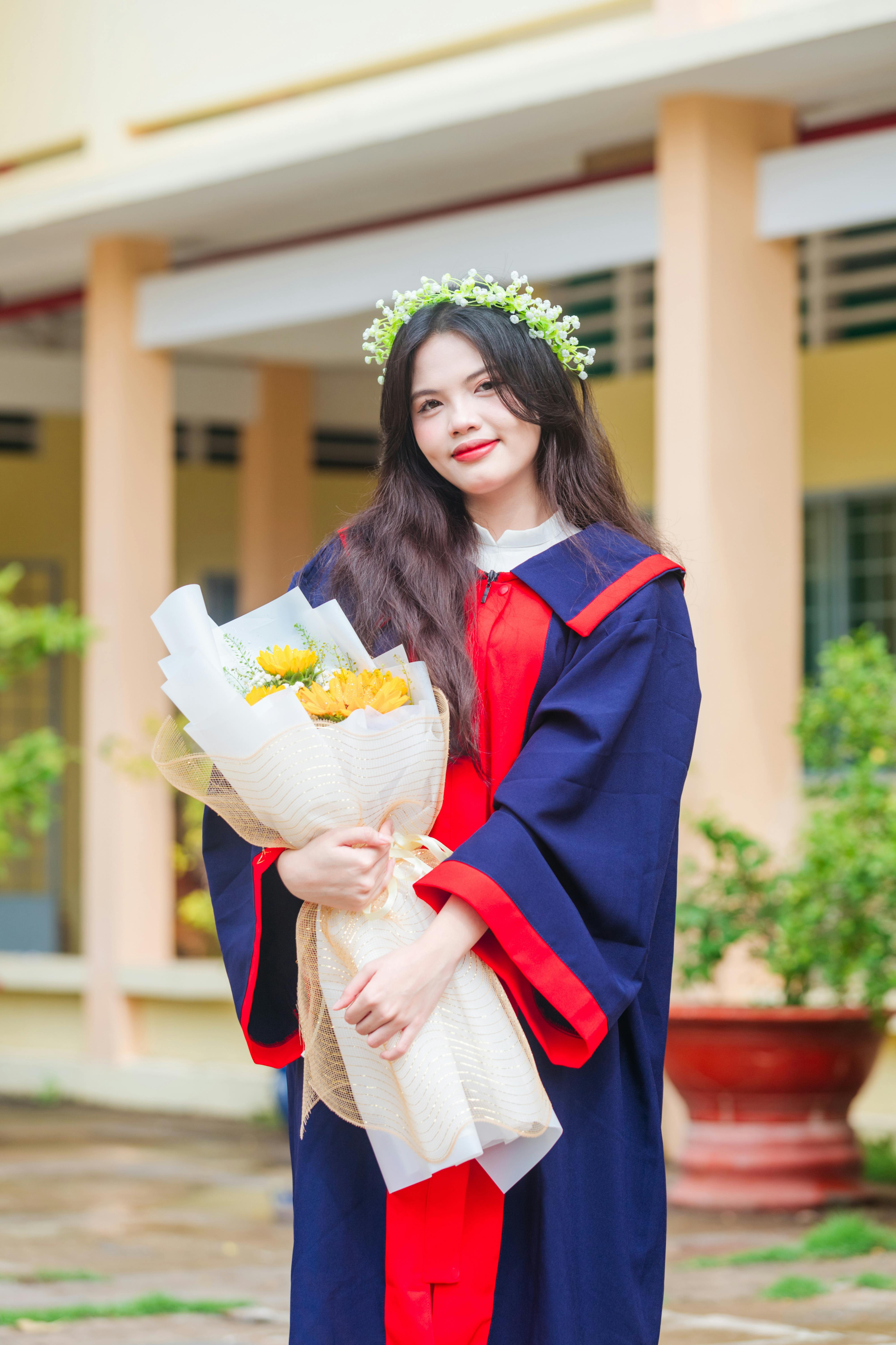 A woman in a graduation gown holding flowers · Free Stock Photo