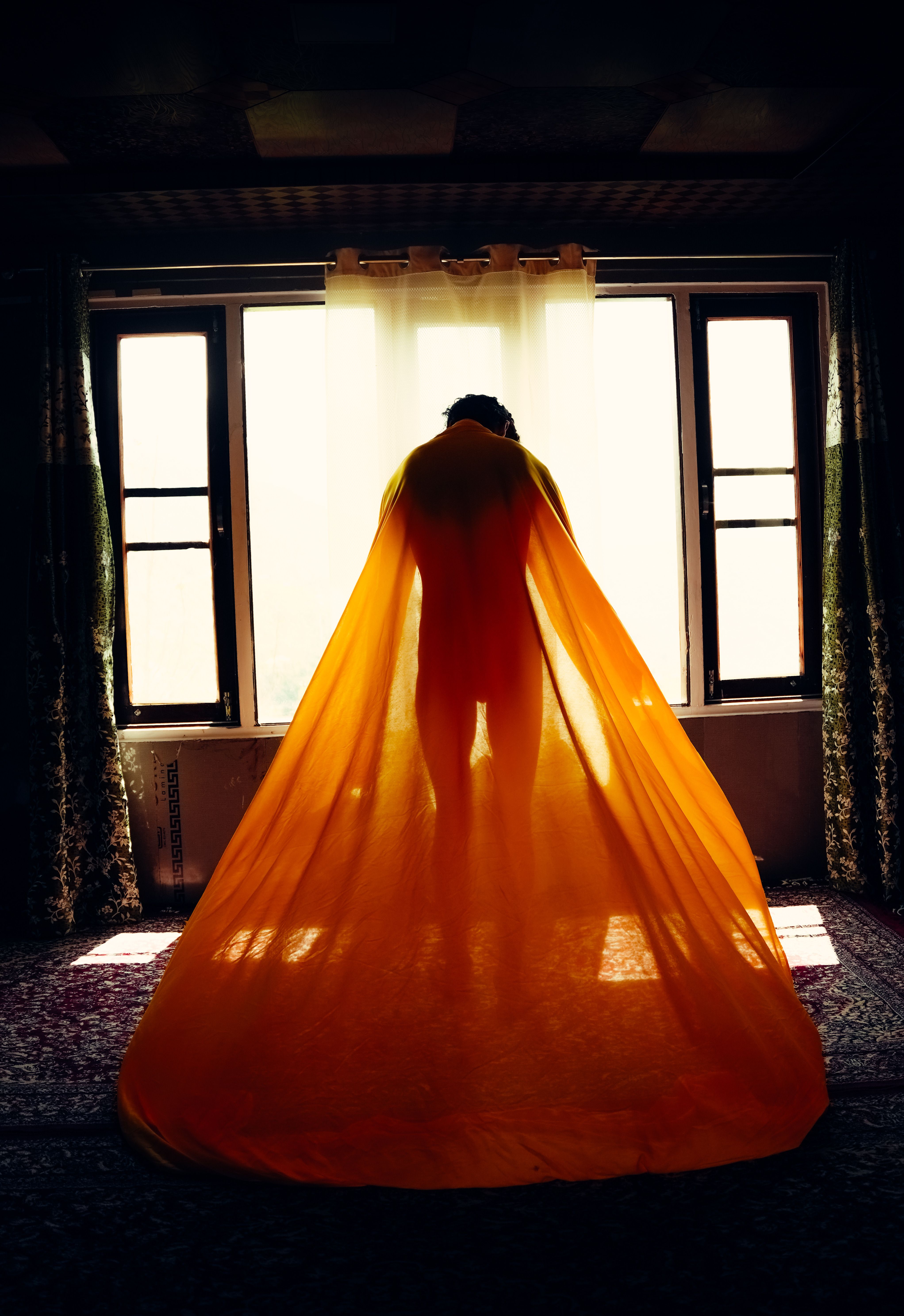 Person Wrapped in Orange Fabric by a Sunlit Window · Free Stock Photo